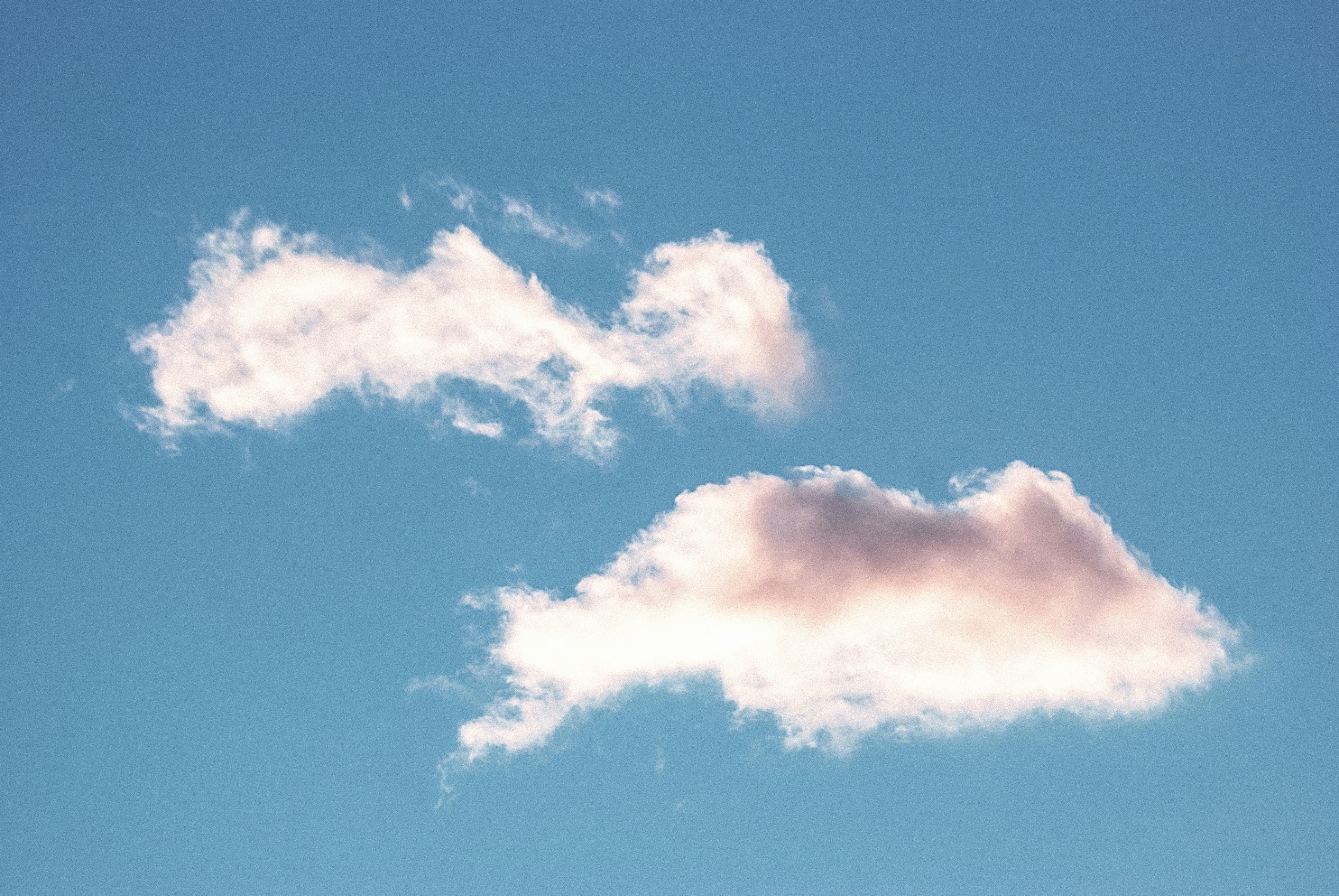 Two soft clouds drift across a clear blue sky, conveying a tranquil, sunlit moment.