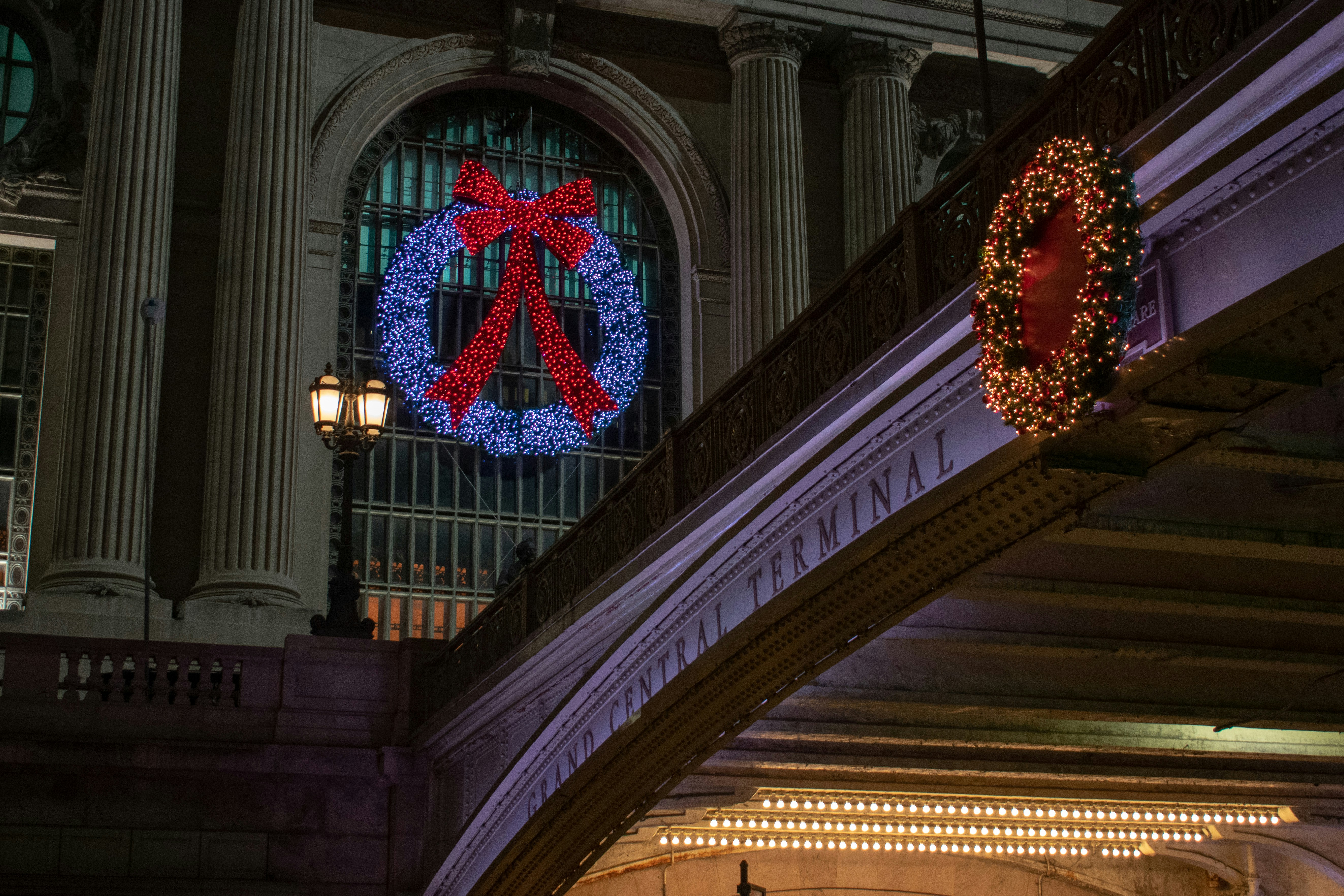 Festive wreaths adorned with lights and ribbons on the facade of Grand Central Terminal during the holiday season.