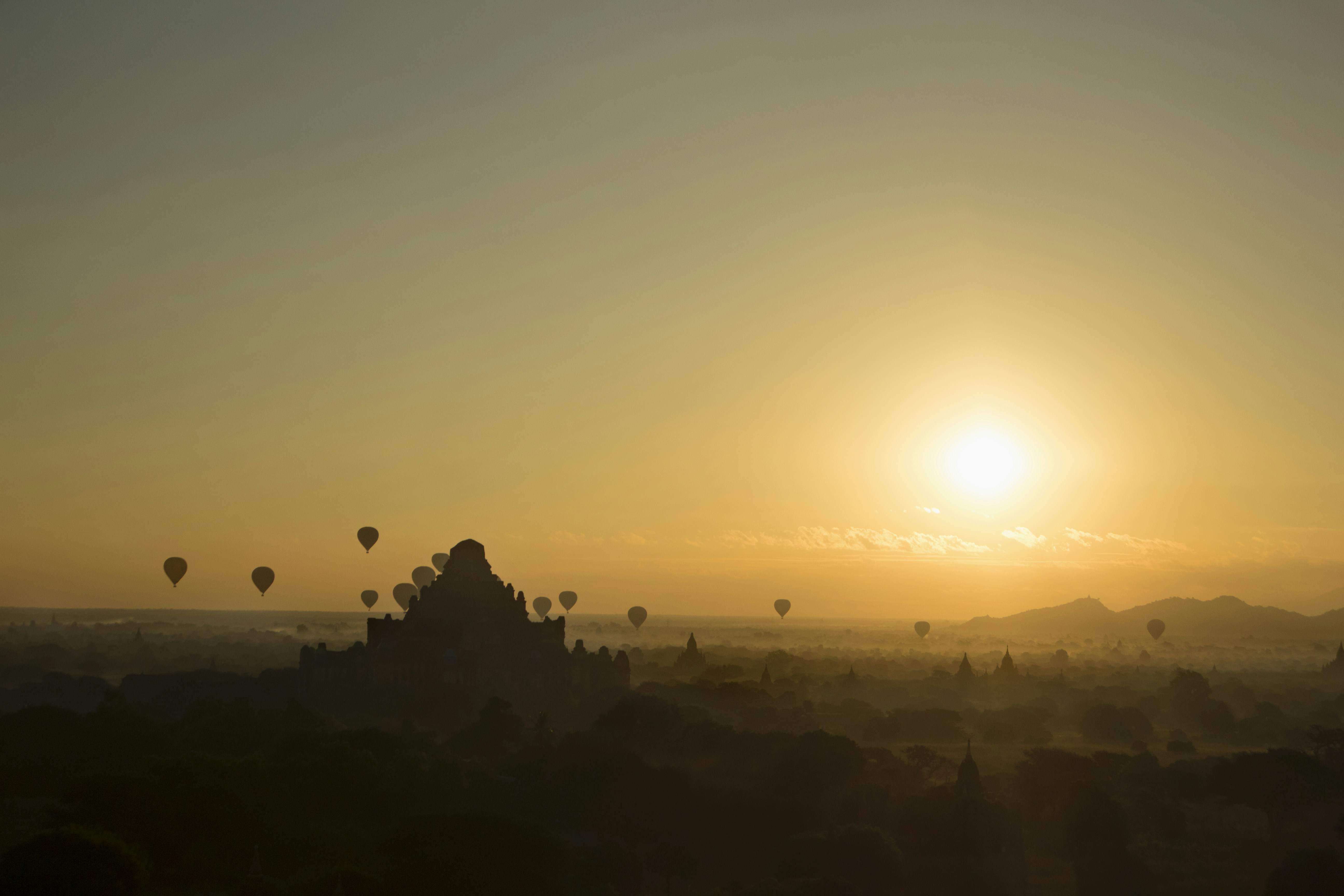 Hot air balloons drift over ancient temples in Bagan at sunrise.