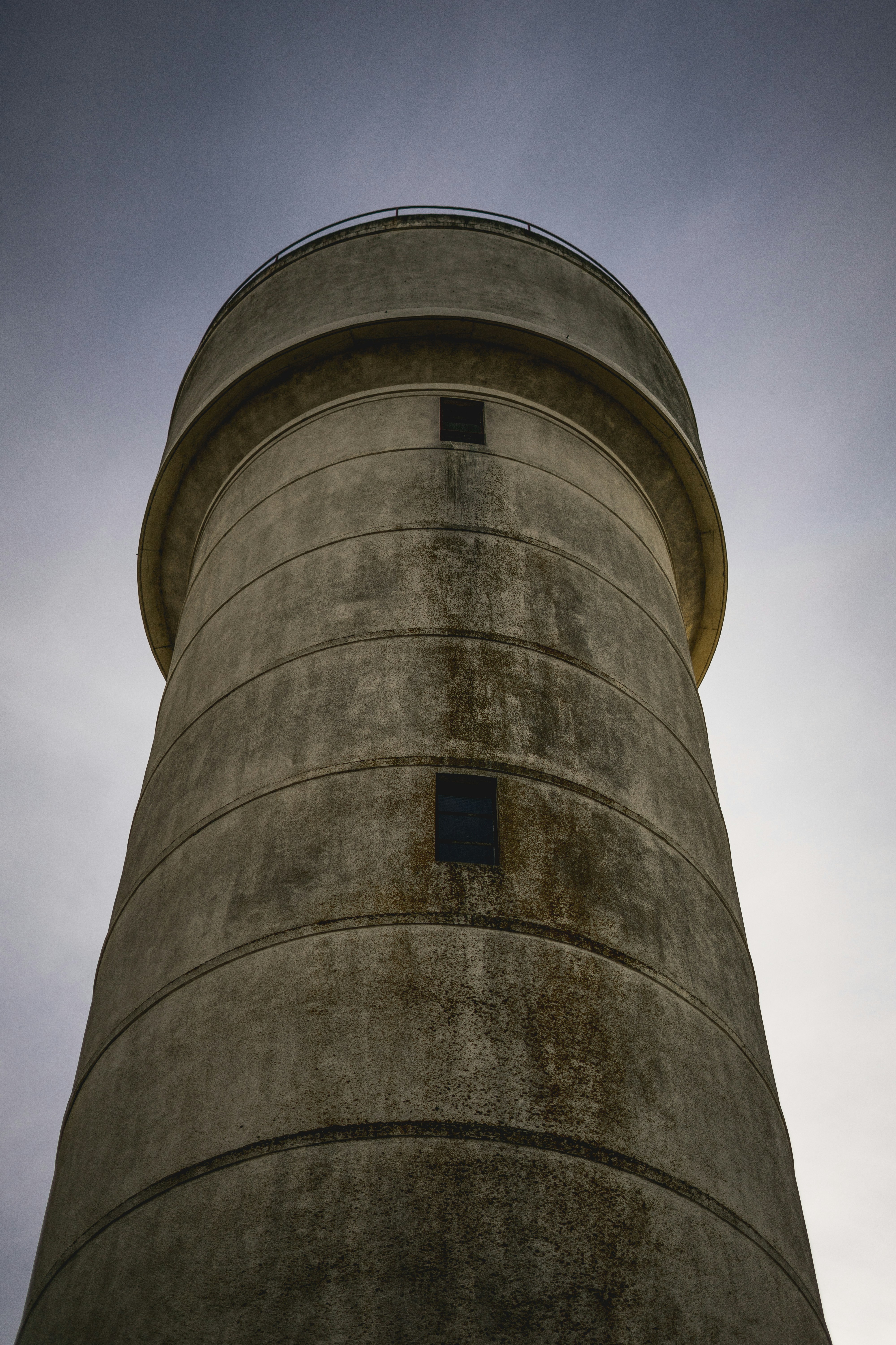 A towering water tower stands against a soft, cloudy sky, showcasing its weathered texture and architectural lines.