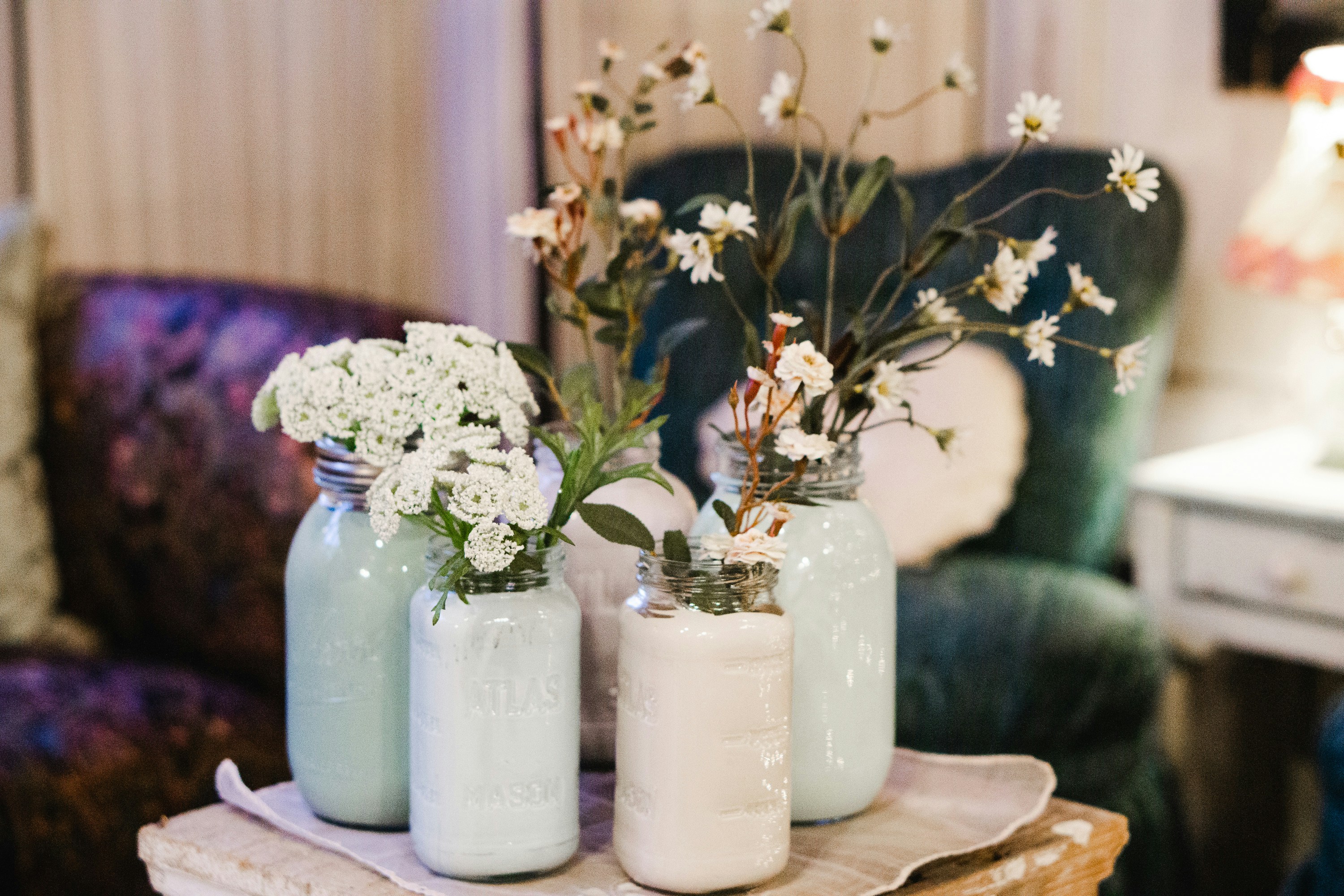 Four glass jars filled with delicate flowers, showcasing a rustic decor style. The arrangement highlights soft pastel colors against a cozy background.