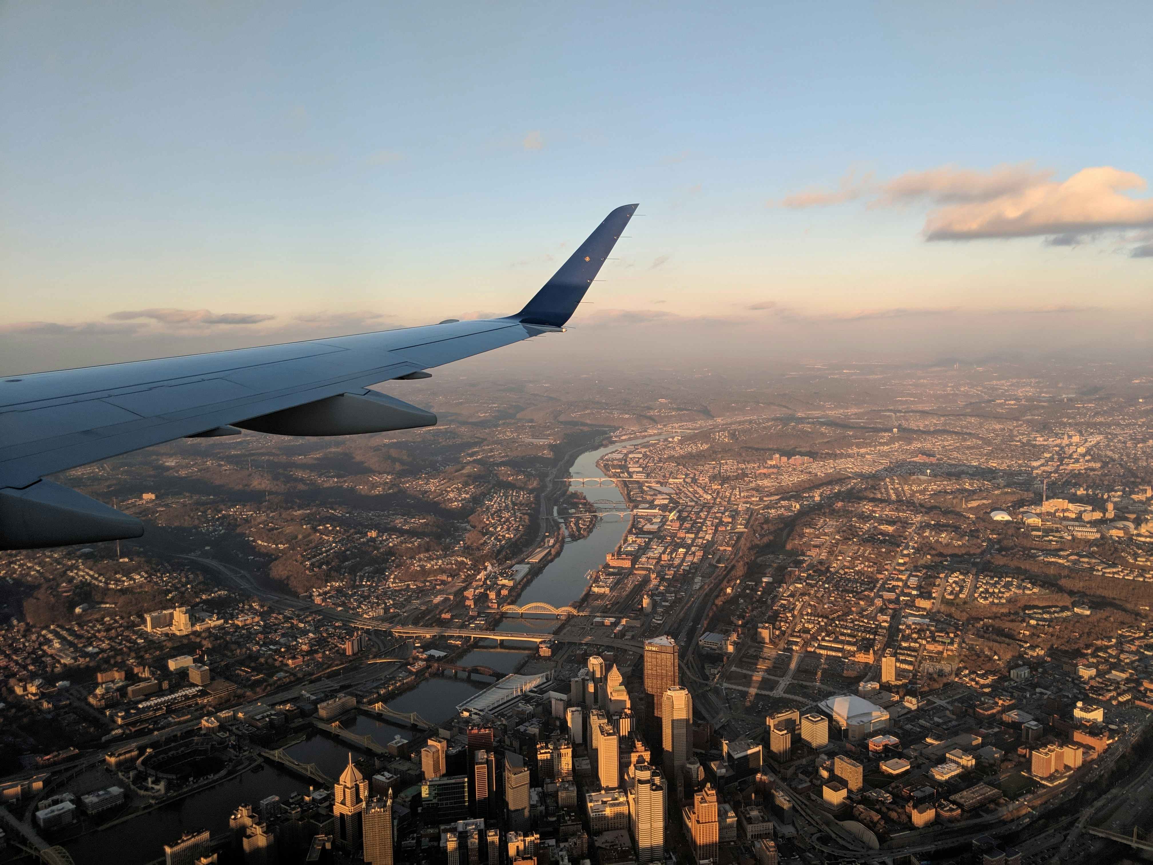 Aerial view of a river flowing between city buildings under a clear sky with a visible airplane wing.
