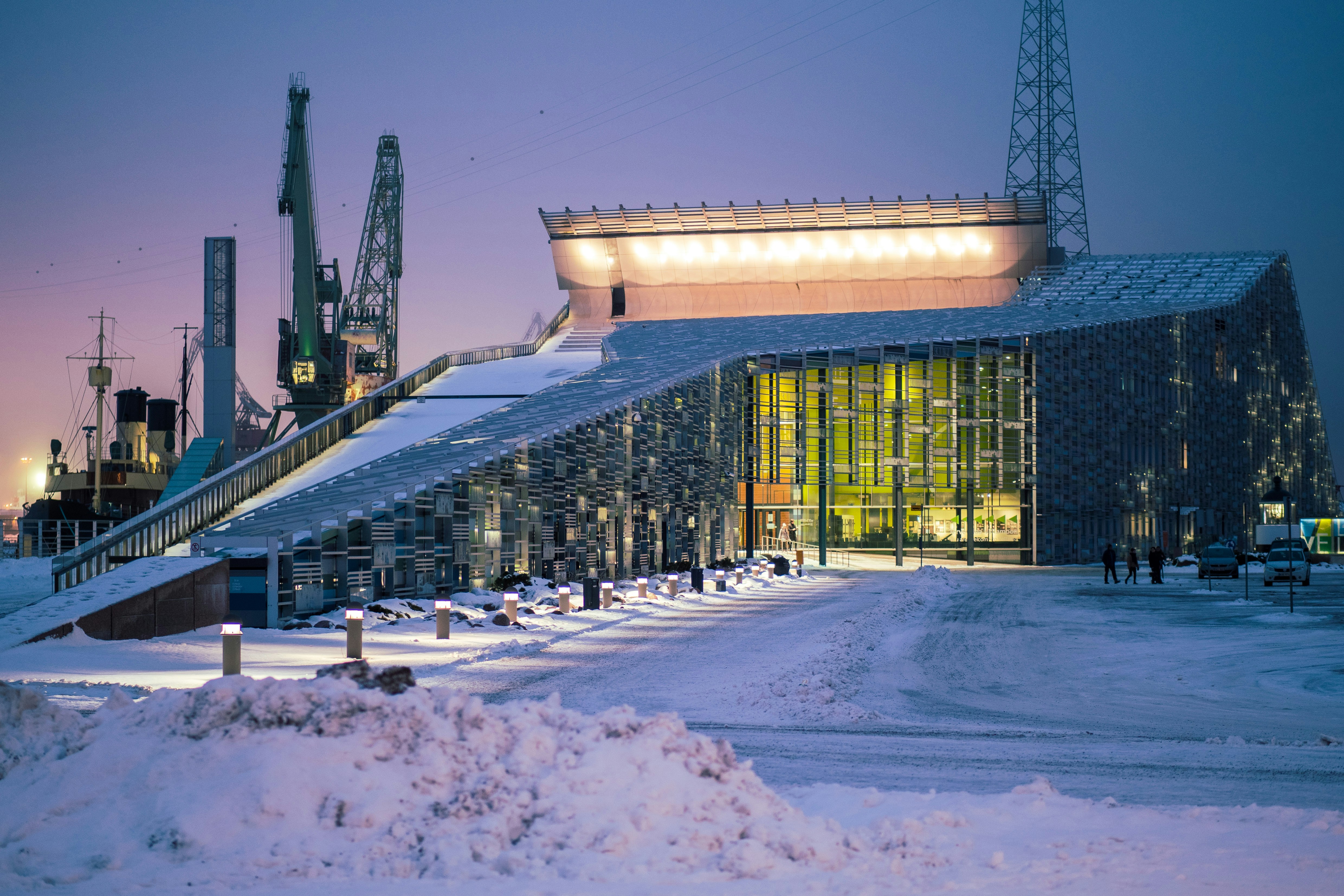 Modern architectural design of the Maritime Museum of Finland, glowing warmly against a snowy twilight backdrop.