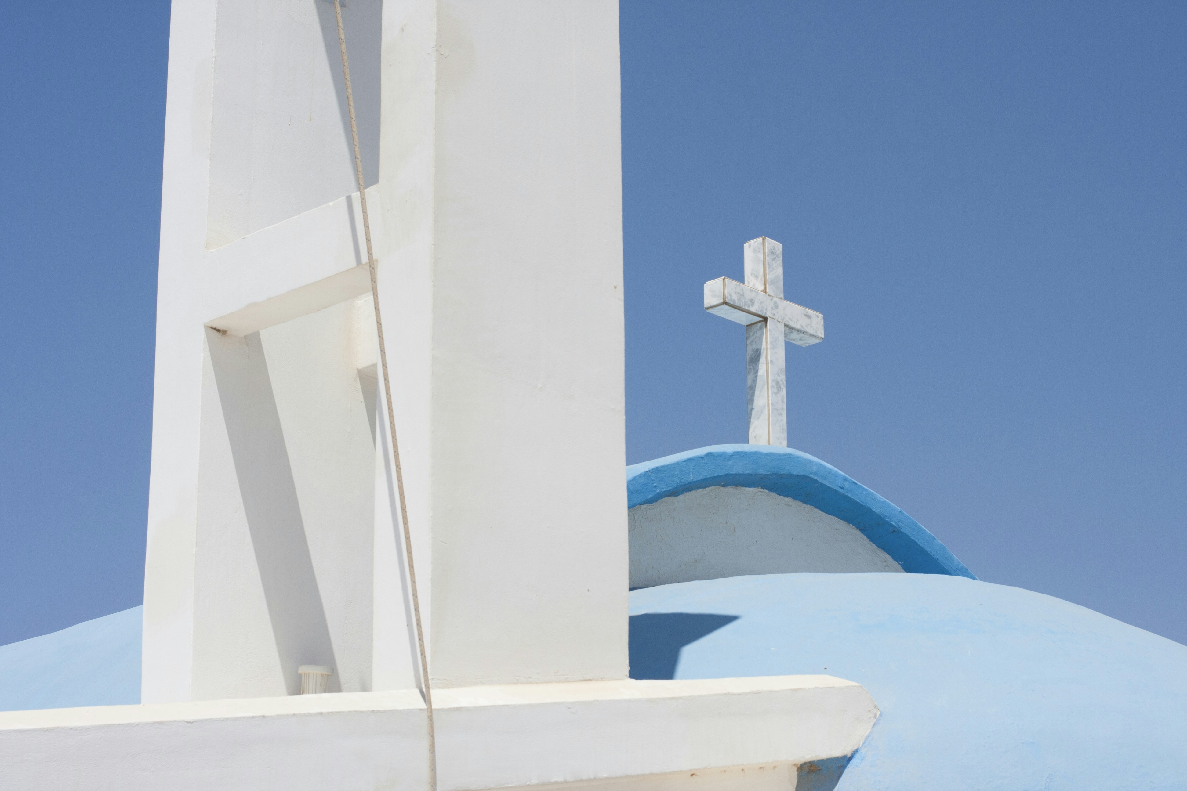 White cross on a blue-domed building under a clear sky.