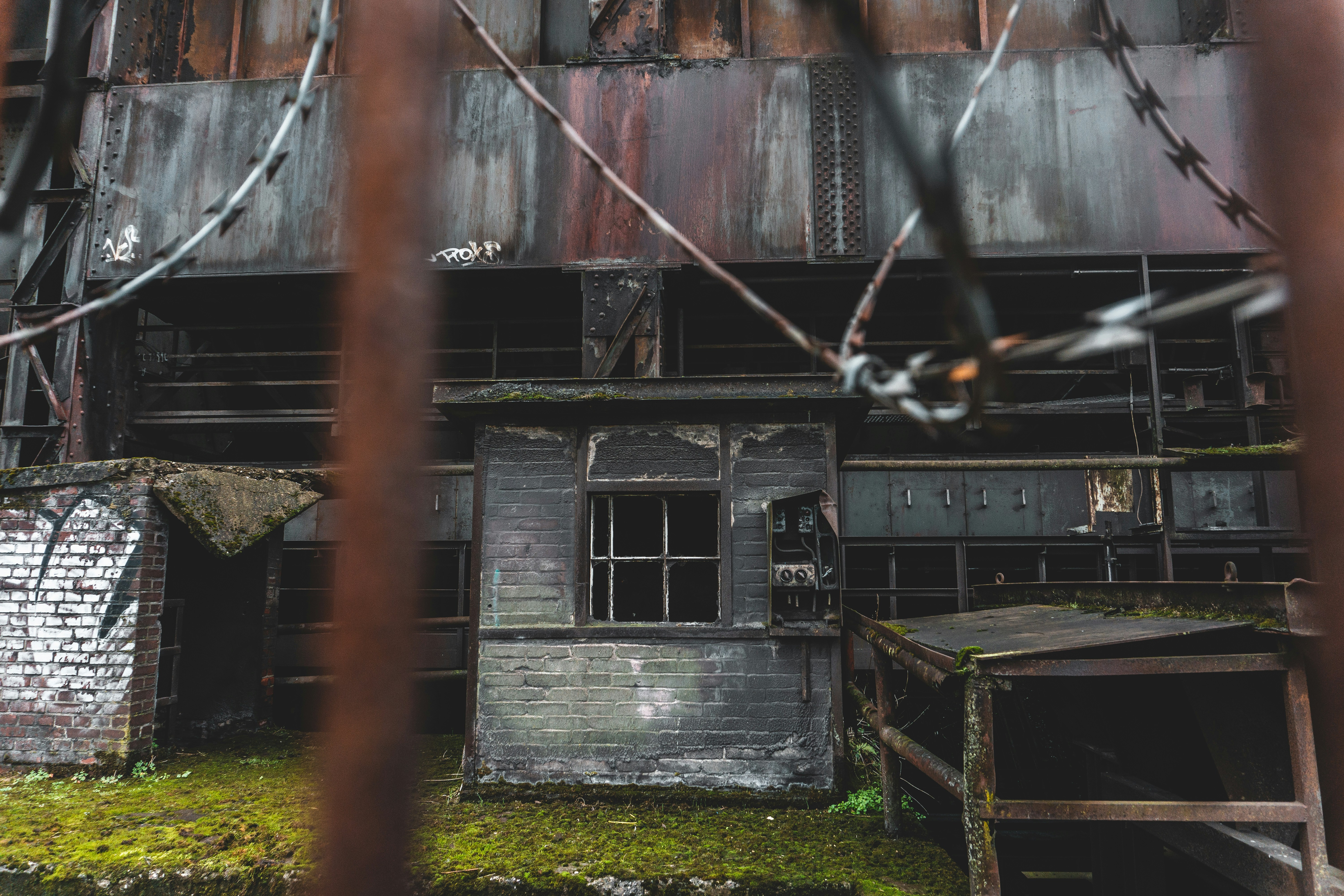 A dilapidated wooden structure with a broken window, partially obscured by rusted metal bars.