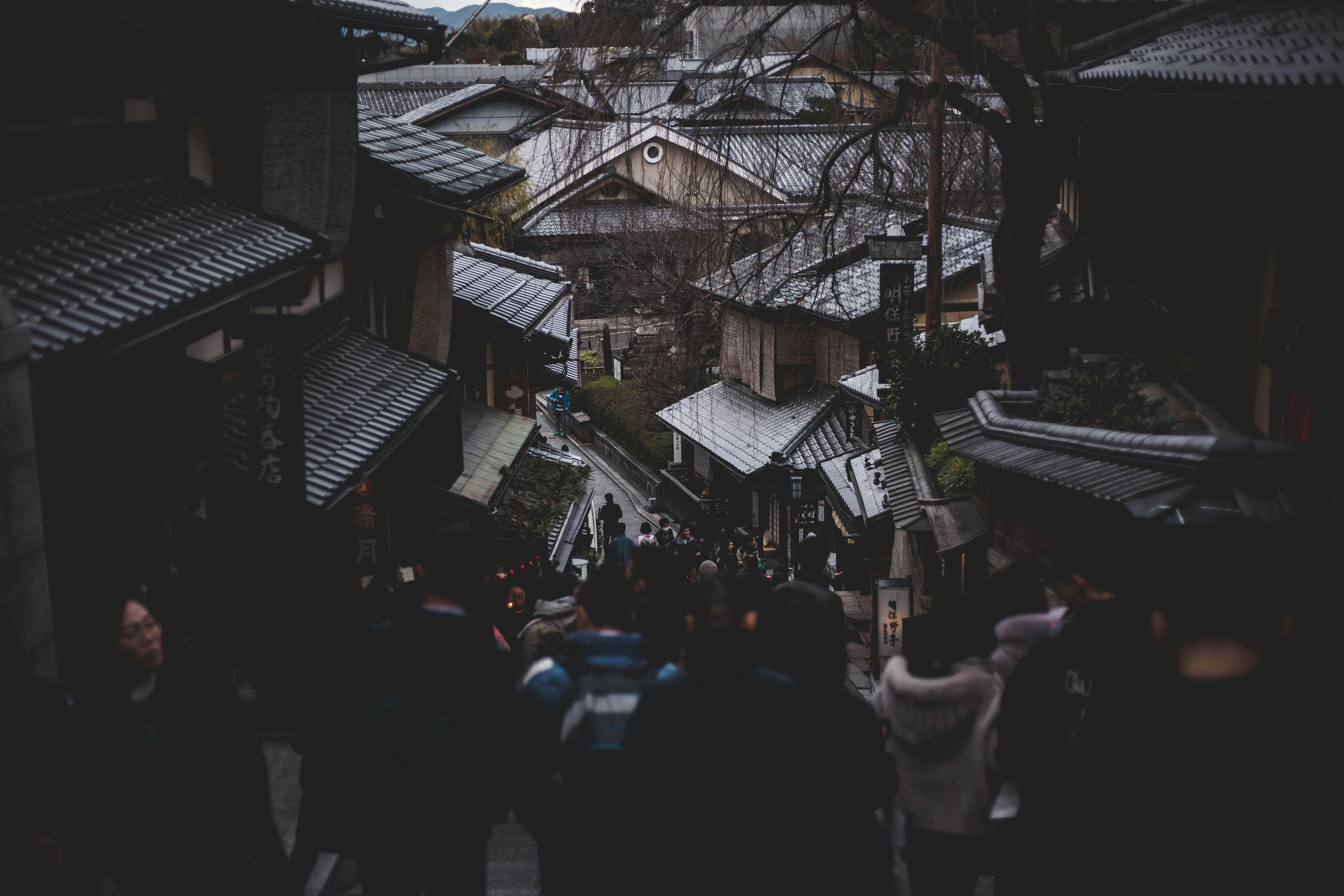 Crowd of people navigating a narrow street lined with traditional wooden buildings and tiled roofs, evoking a sense of history and culture.