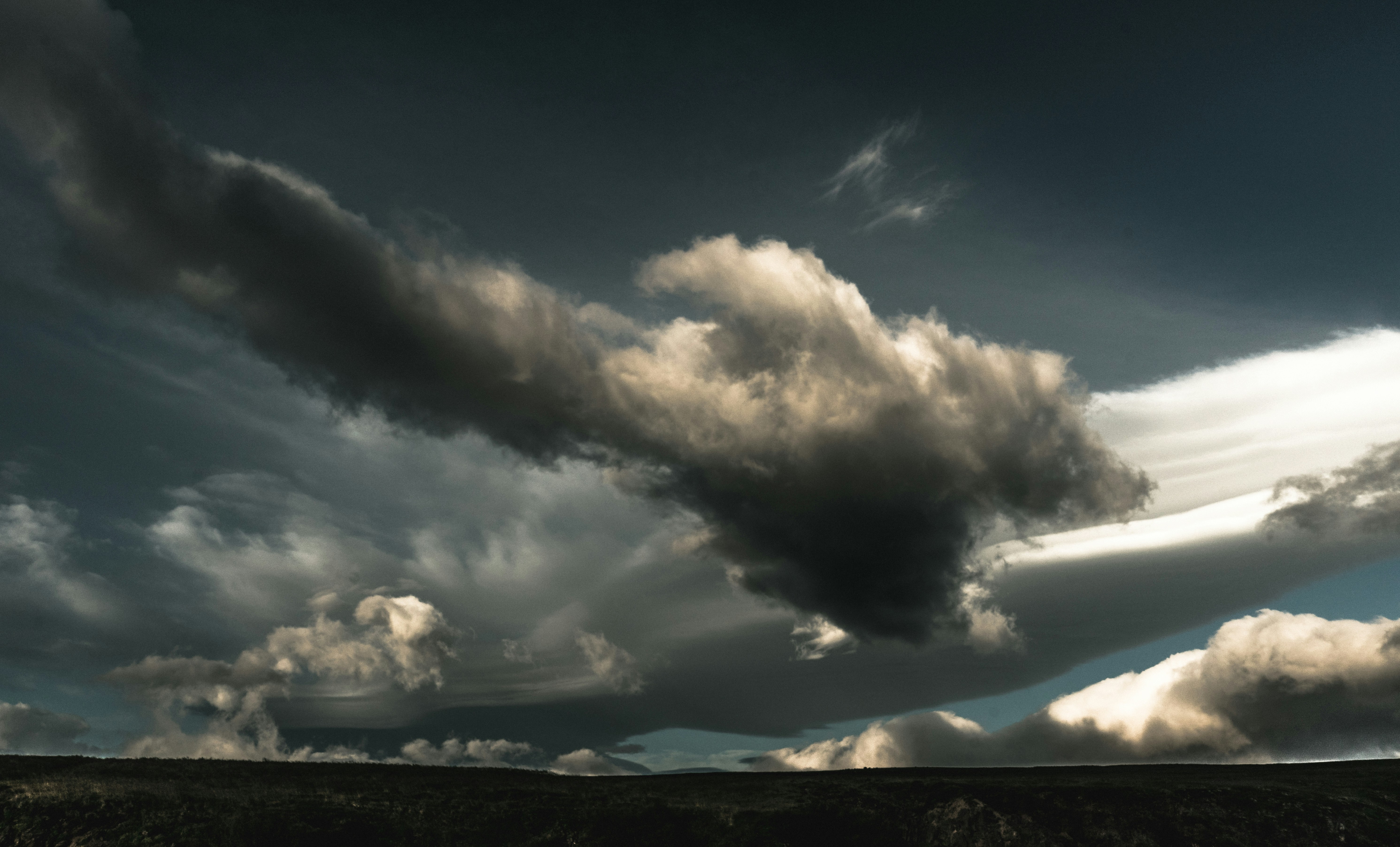 Moody grey and black clouds swirling over a dark horizon, creating a dramatic sky scene.