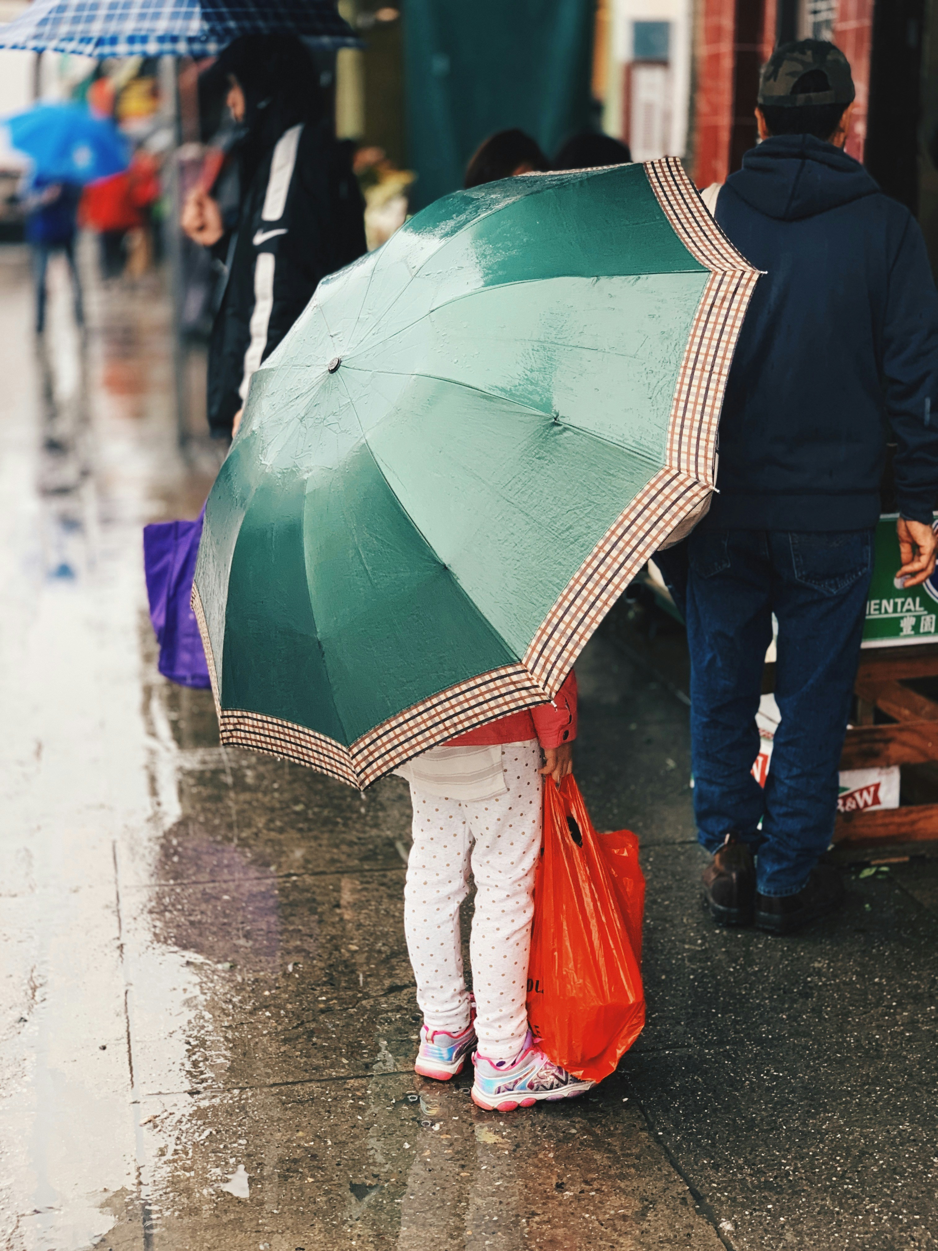 Green Umbrella in a Rain-Soaked Street: Shelter Amid City Rush