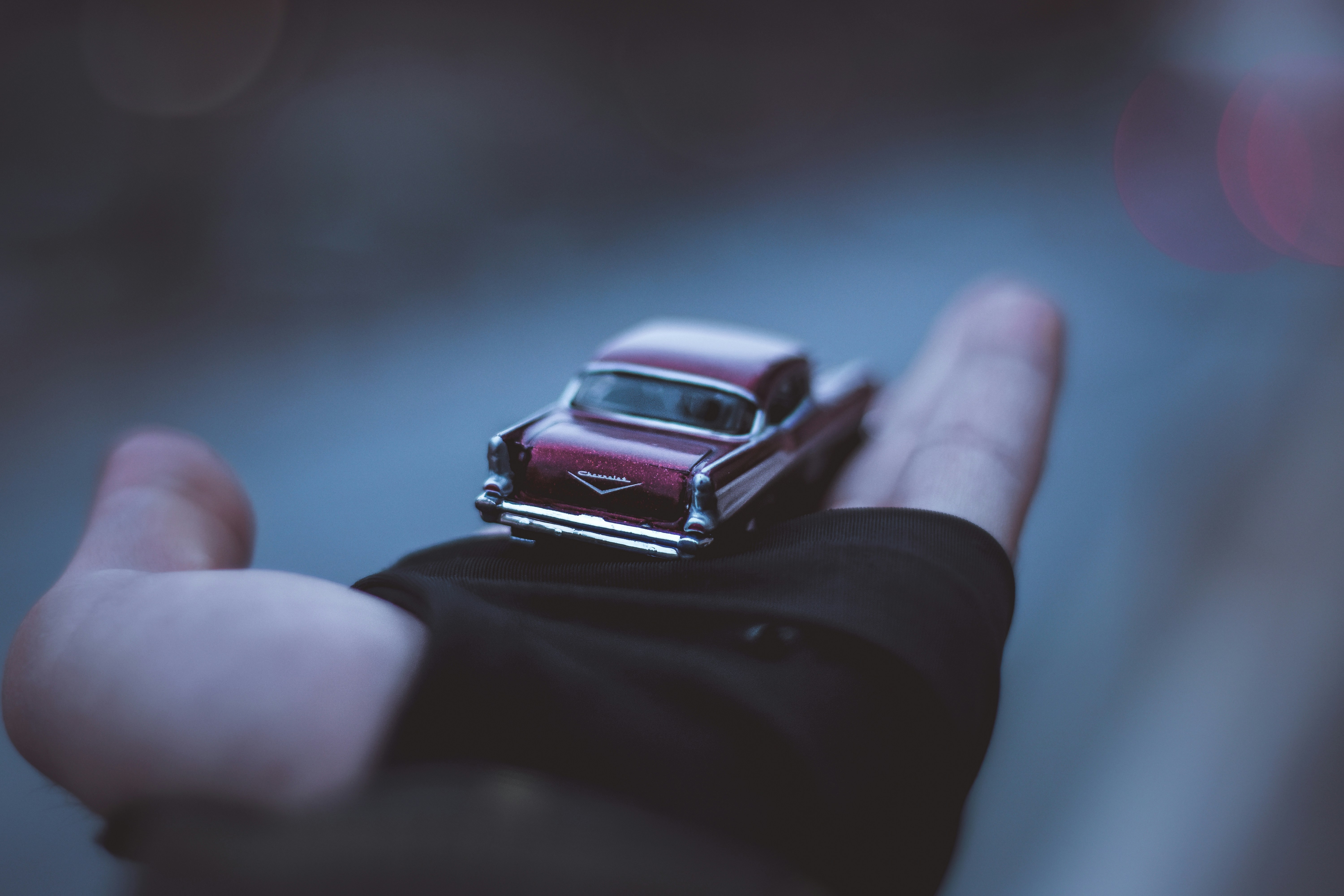 Palm-Sized Crimson Classic: A Tiny Car Cradled in Velvet Blue Blur