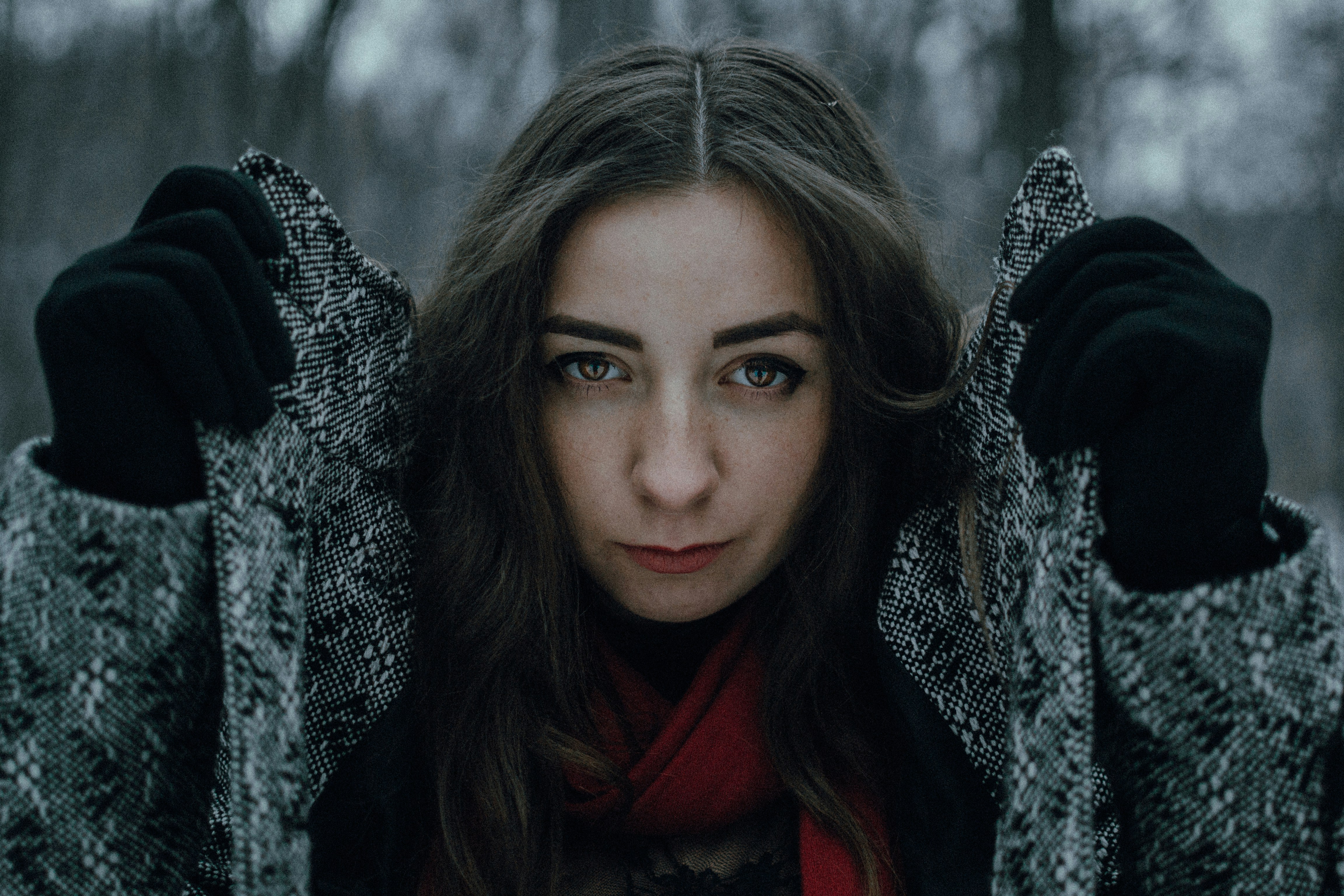 A woman with a determined expression pulls her coat closer against the cold, set against a muted winter backdrop.