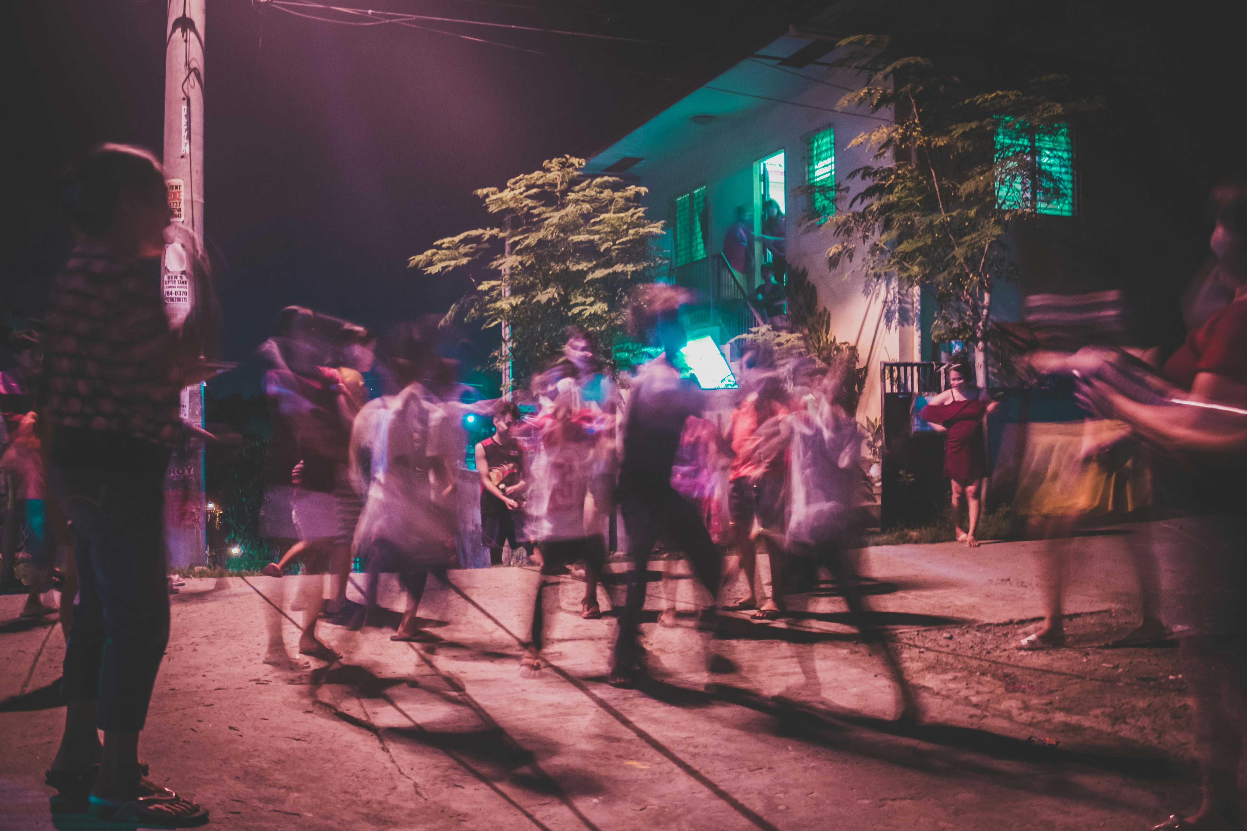 Children dancing joyfully on a dimly lit street, with blurred motion conveying the energy of the moment. The scene is illuminated by soft lights from a nearby house.