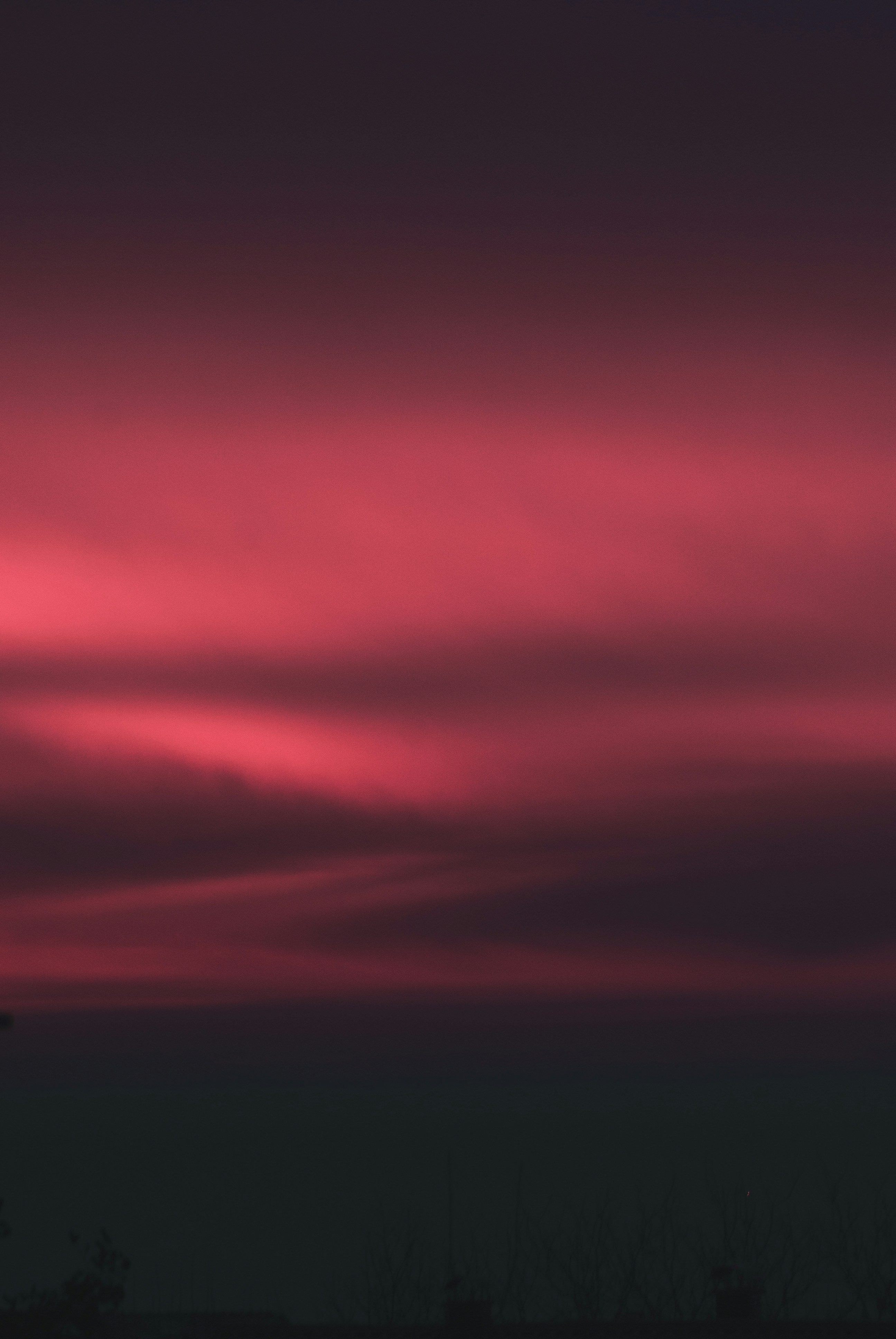 Pink sunset sky spills across a dark horizon, with soft cloud bands and silhouettes along the foreground.