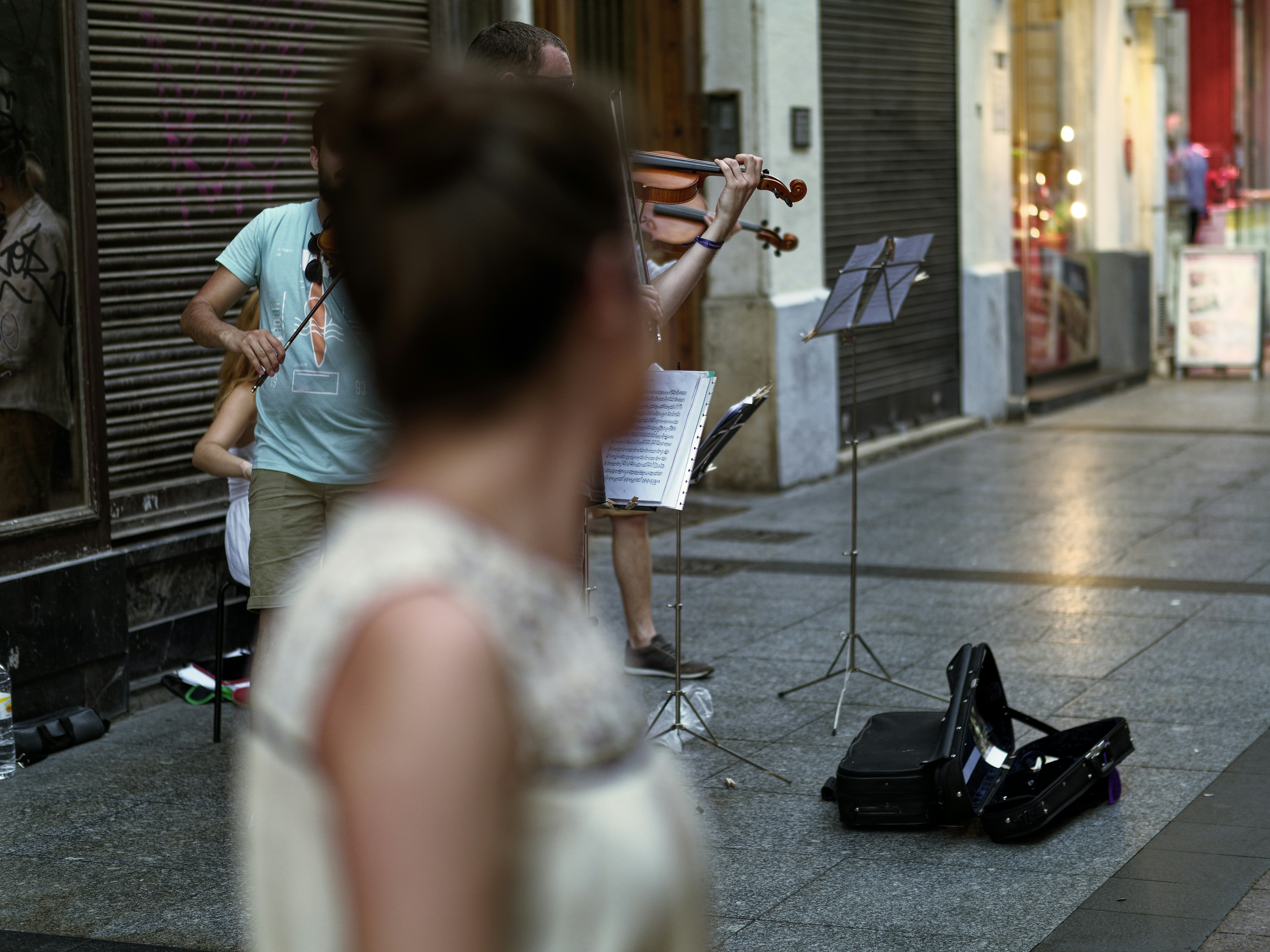 Violinist performing on a city street as a passerby moves through the foreground.
