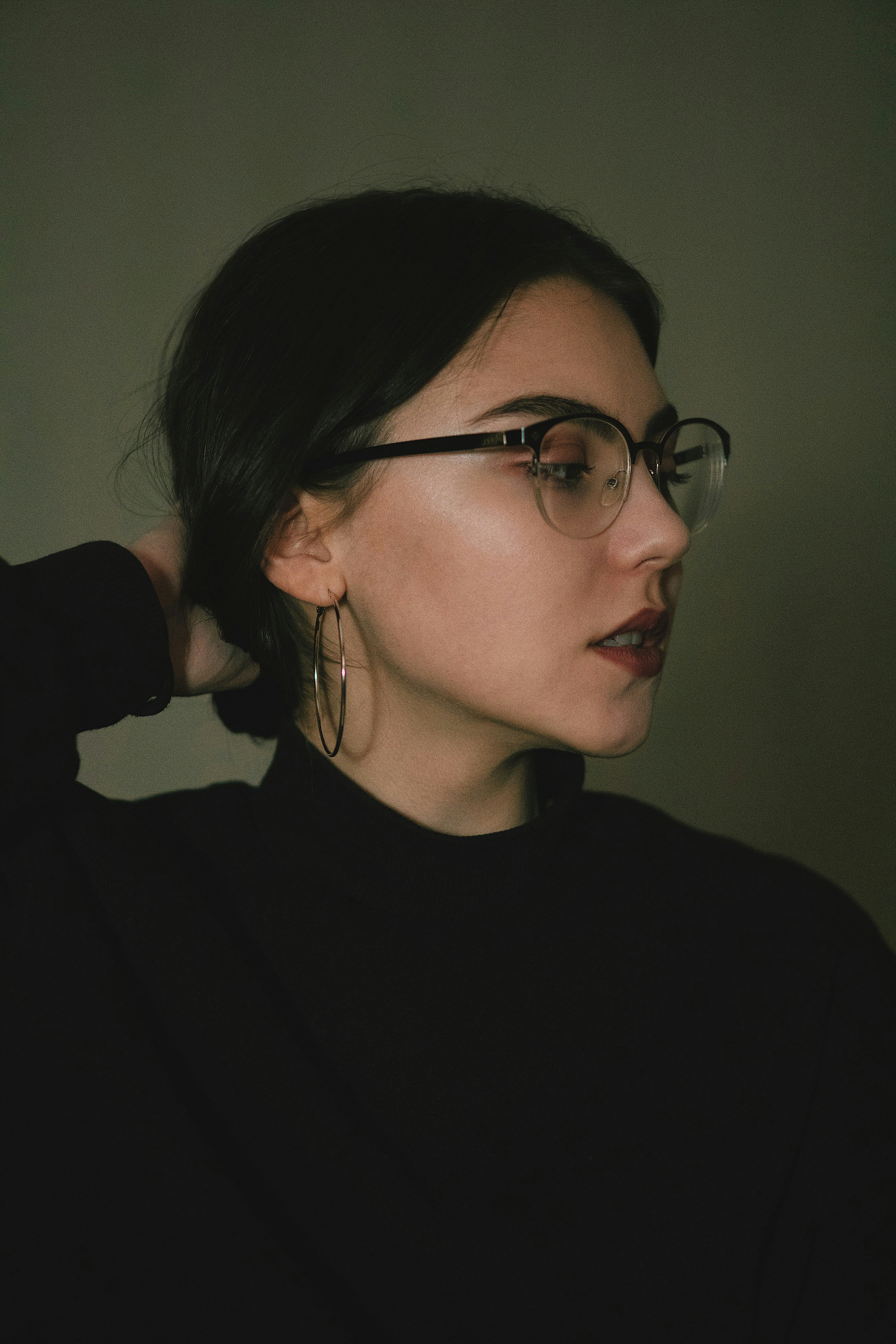 Profile of a woman with glasses and hoop earrings, showcasing a contemplative expression against a muted background.