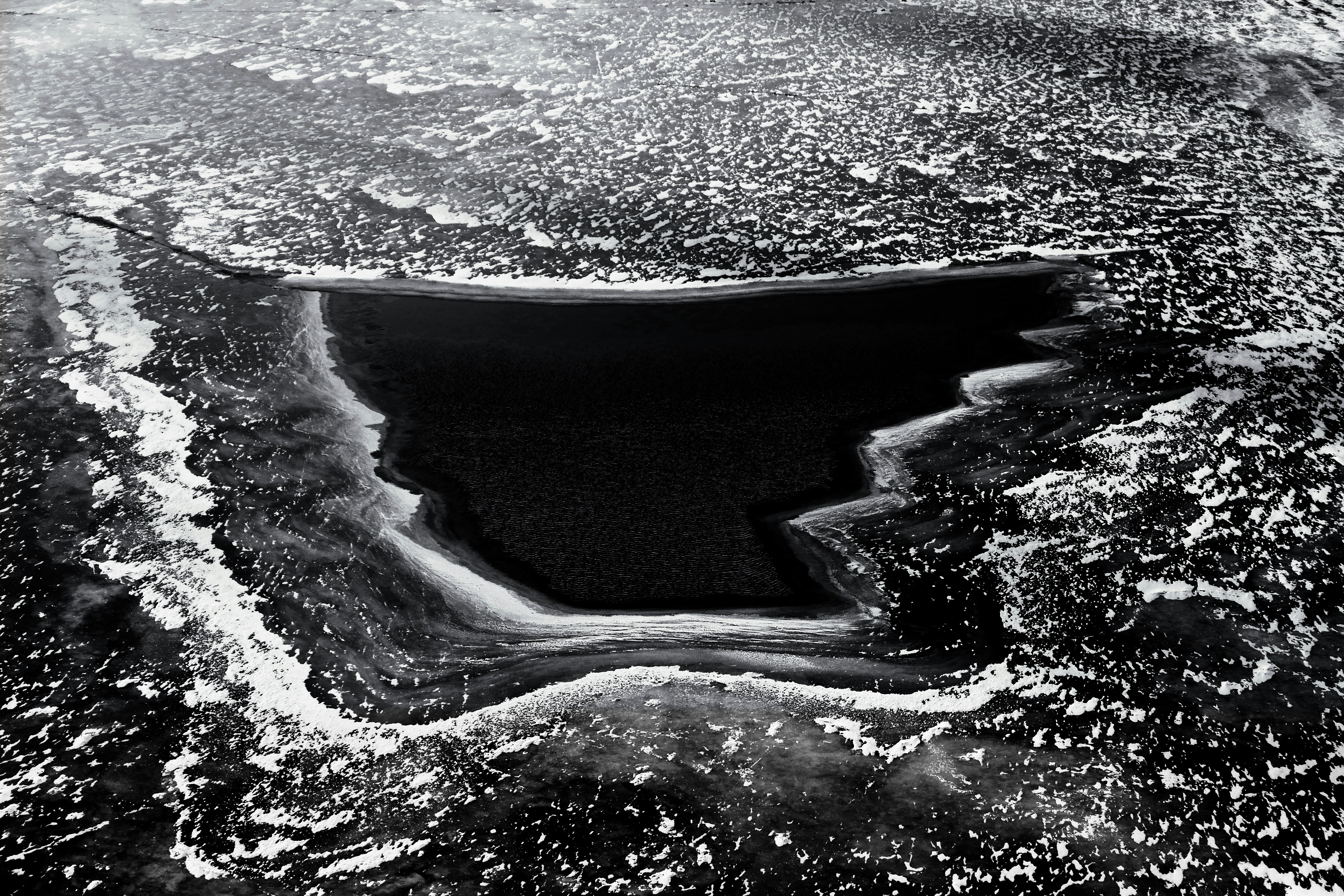 Aerial view of a geometric ice formation with a deep, dark central cavity surrounded by textured frozen surfaces.