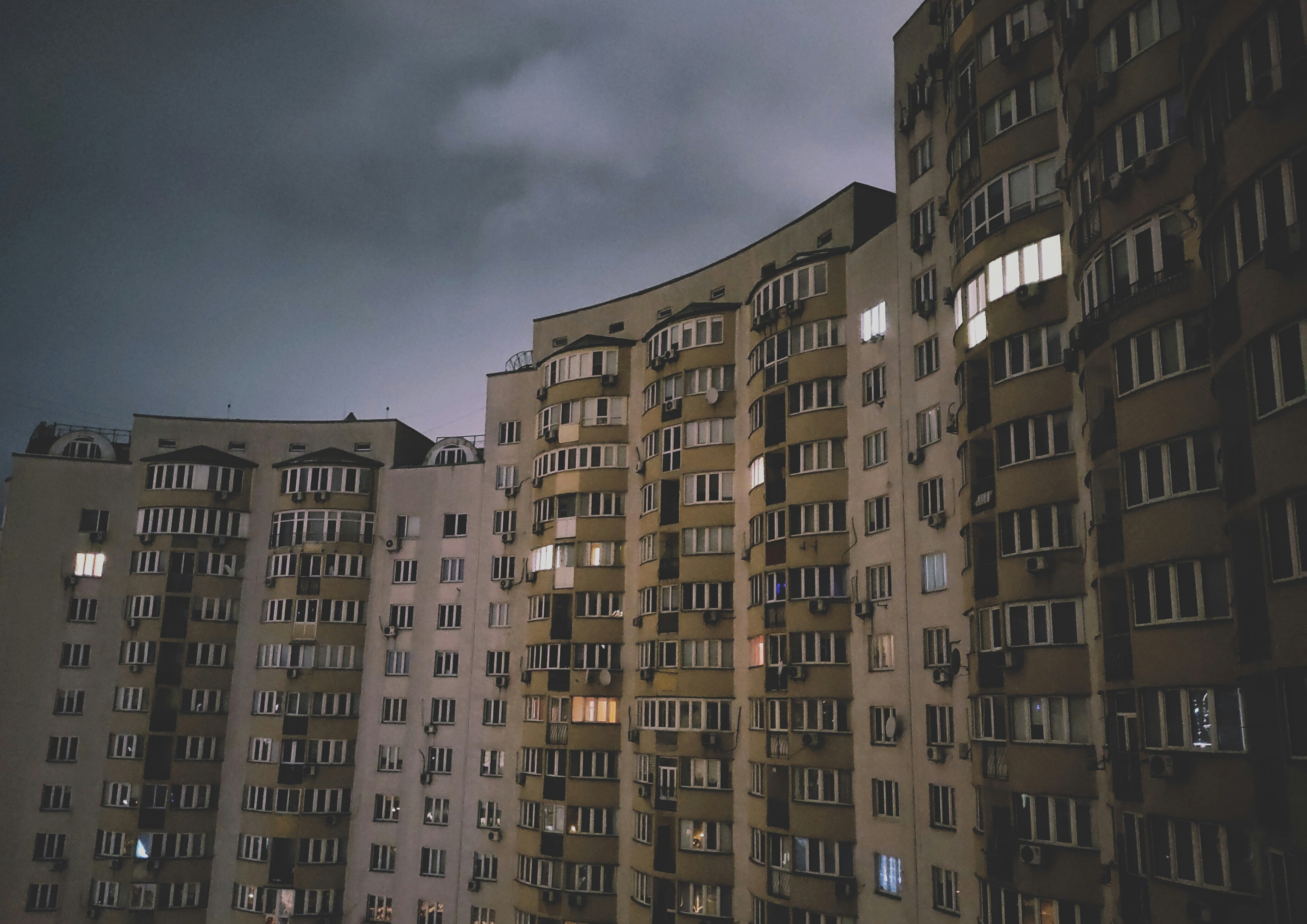 Illuminated apartment windows contrast against a moody sky, showcasing urban architecture at dusk.