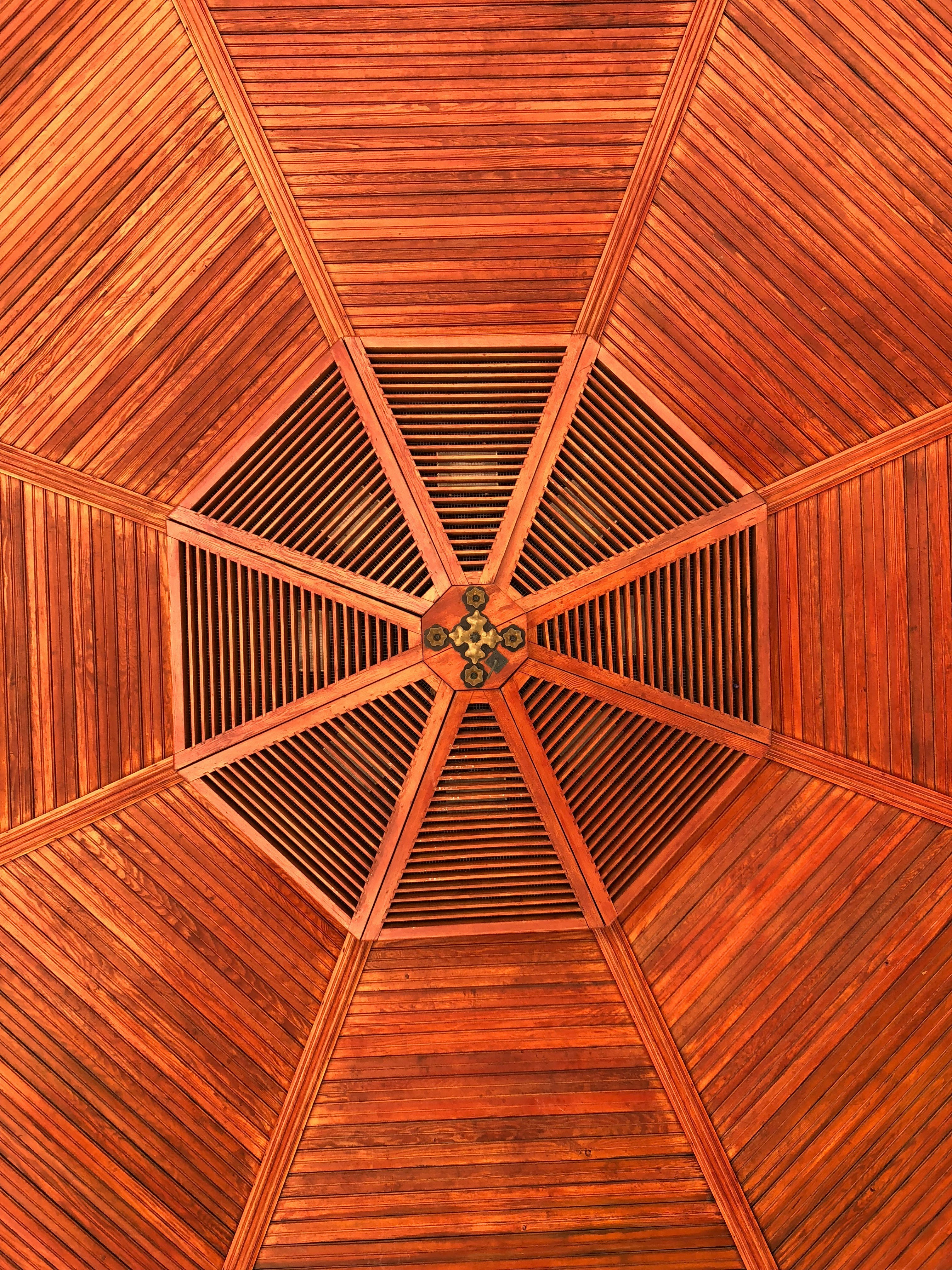 Intricate wooden ceiling design featuring a symmetrical pattern with alternating slats and solid sections. The central floral motif adds a touch of elegance.