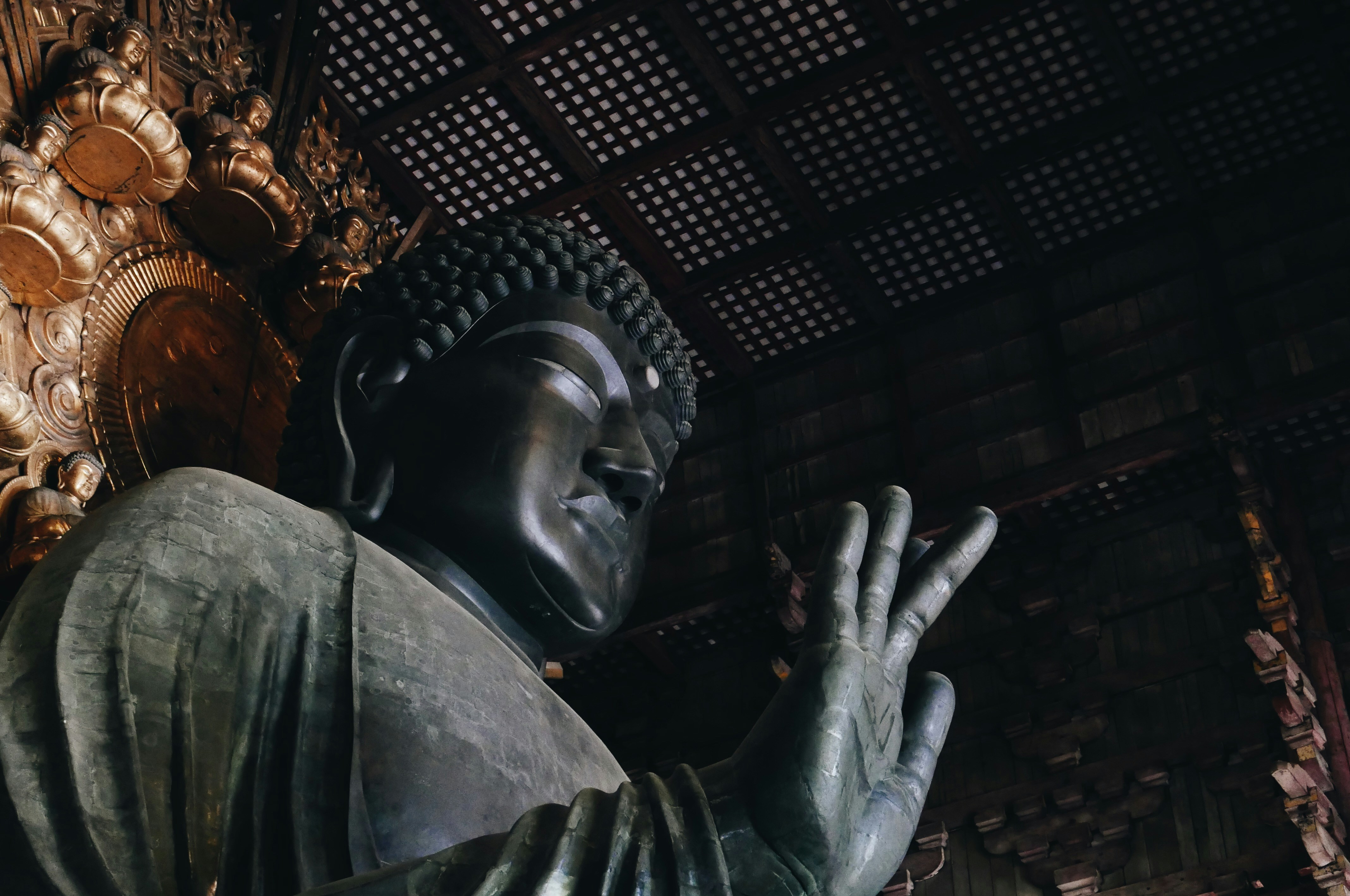 Black Buddha statue with an intricately detailed backdrop in a dimly lit room.