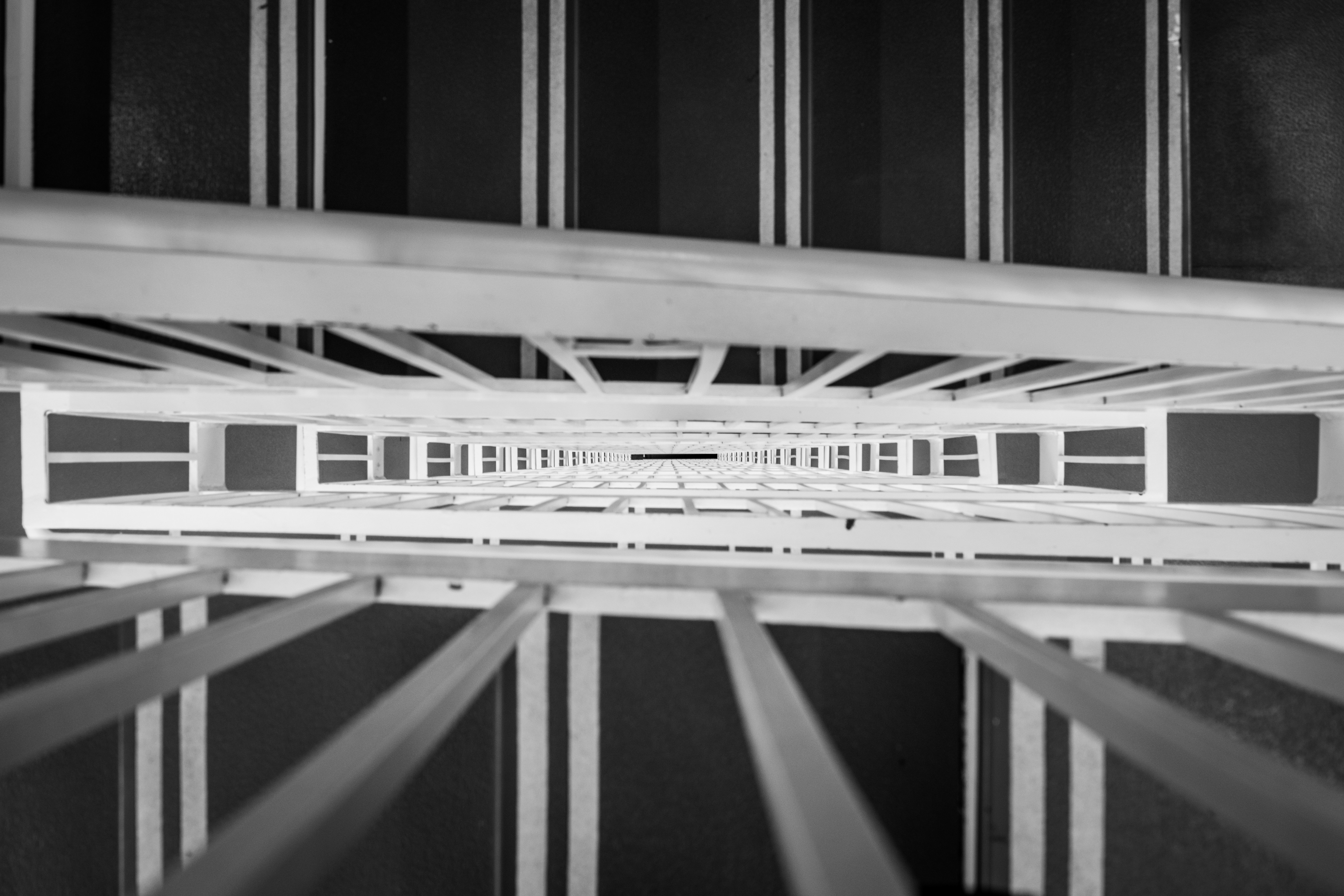 A monochromatic view of a staircase, emphasizing the geometric patterns formed by the railings and steps. The composition draws the eye downward through the structure.