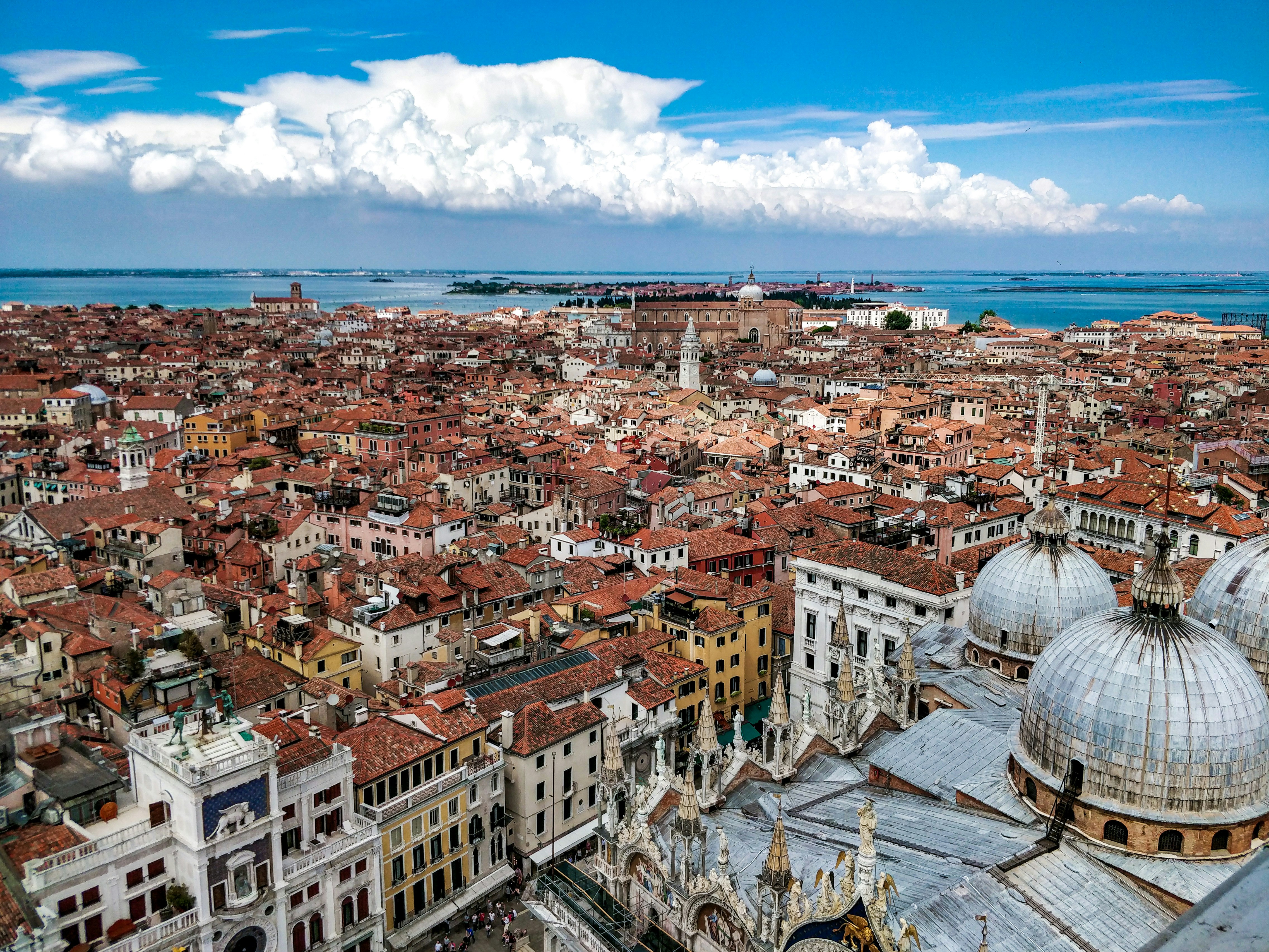 Expansive view of Venice's terracotta rooftops under a vibrant blue sky with fluffy clouds.