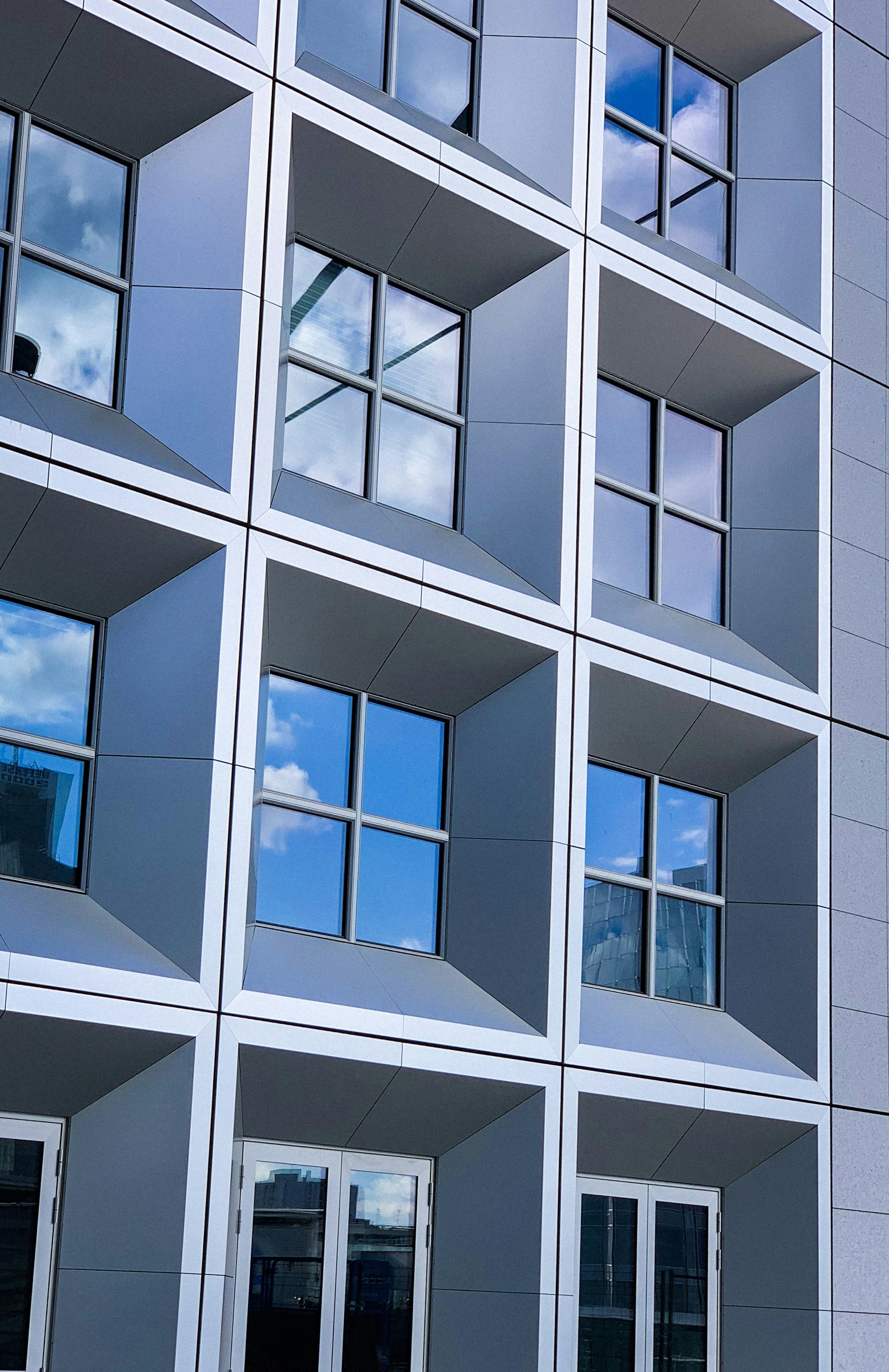 Architectural facade featuring a grid of angular windows reflecting the sky and surrounding buildings.