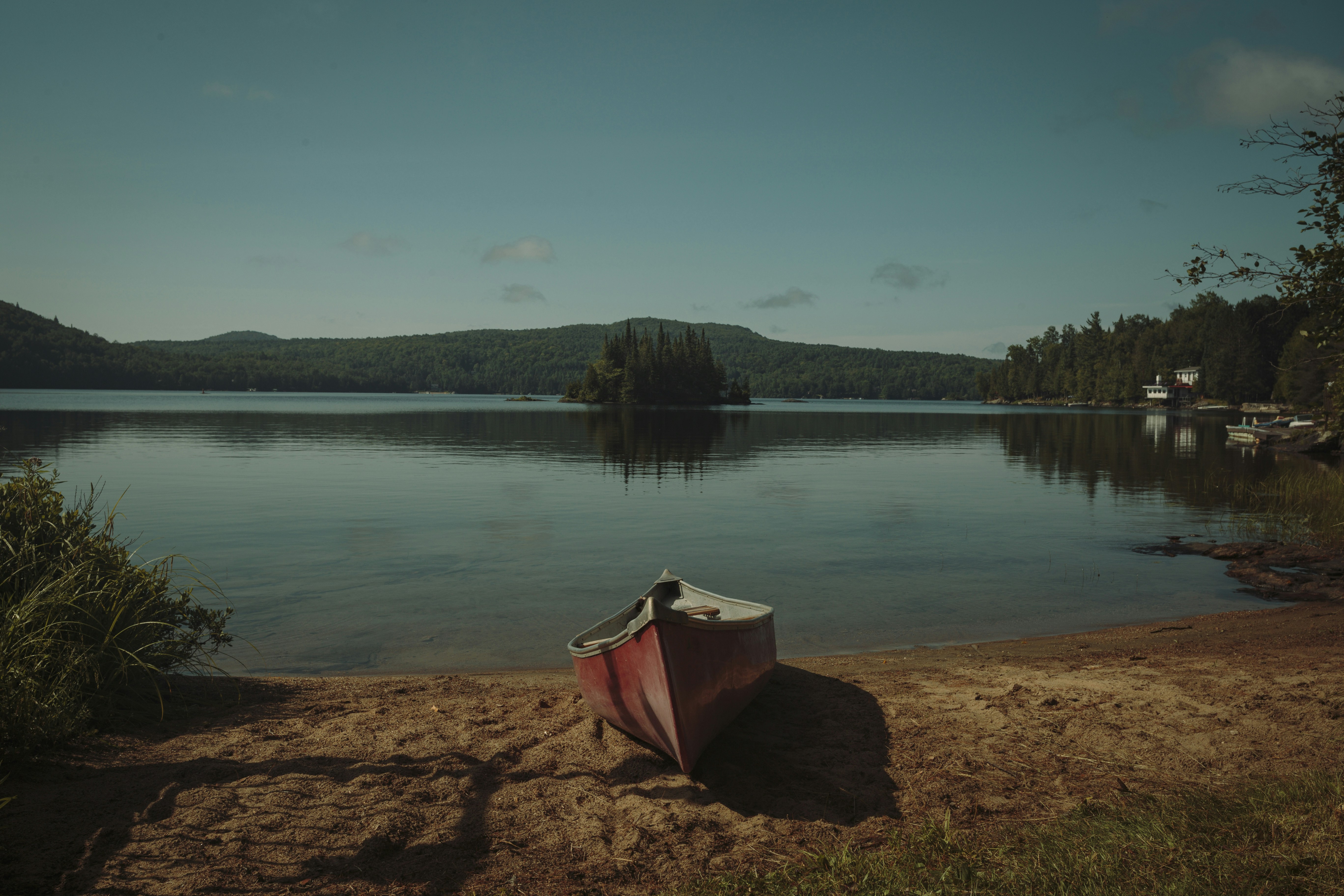 Red Rowboat at the Water's Edge under Quiet Lake Skies