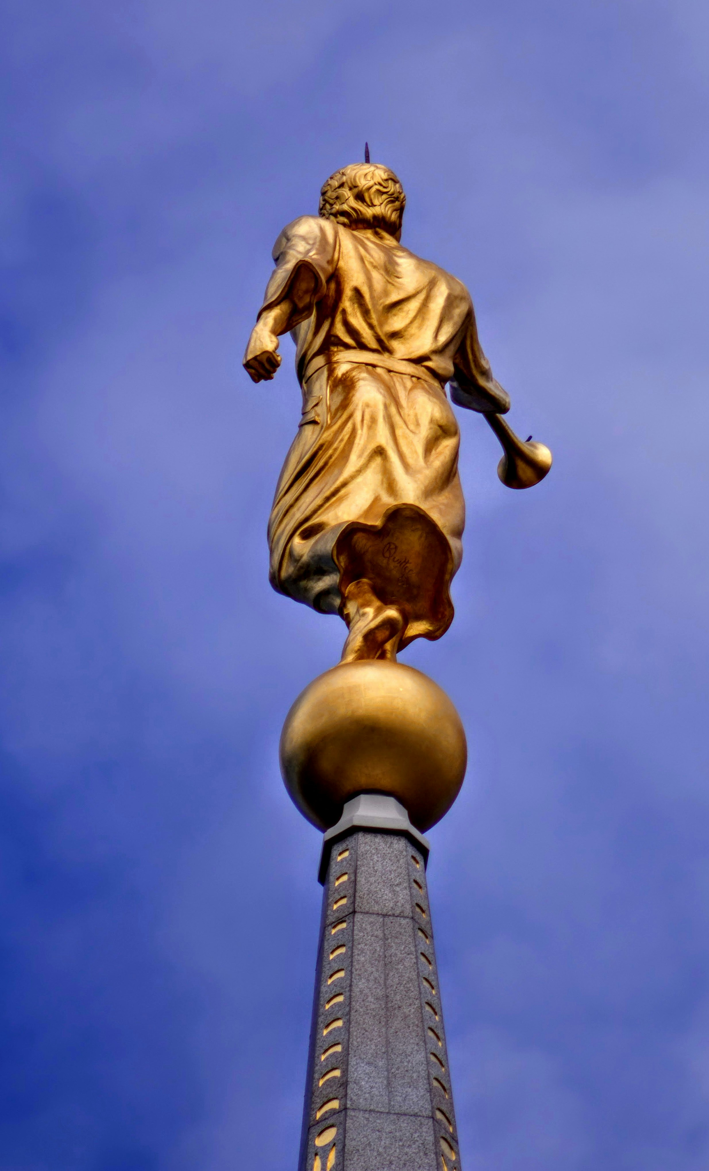 A golden statue stands atop a tall column, capturing the essence of strength and grace against a blue sky.