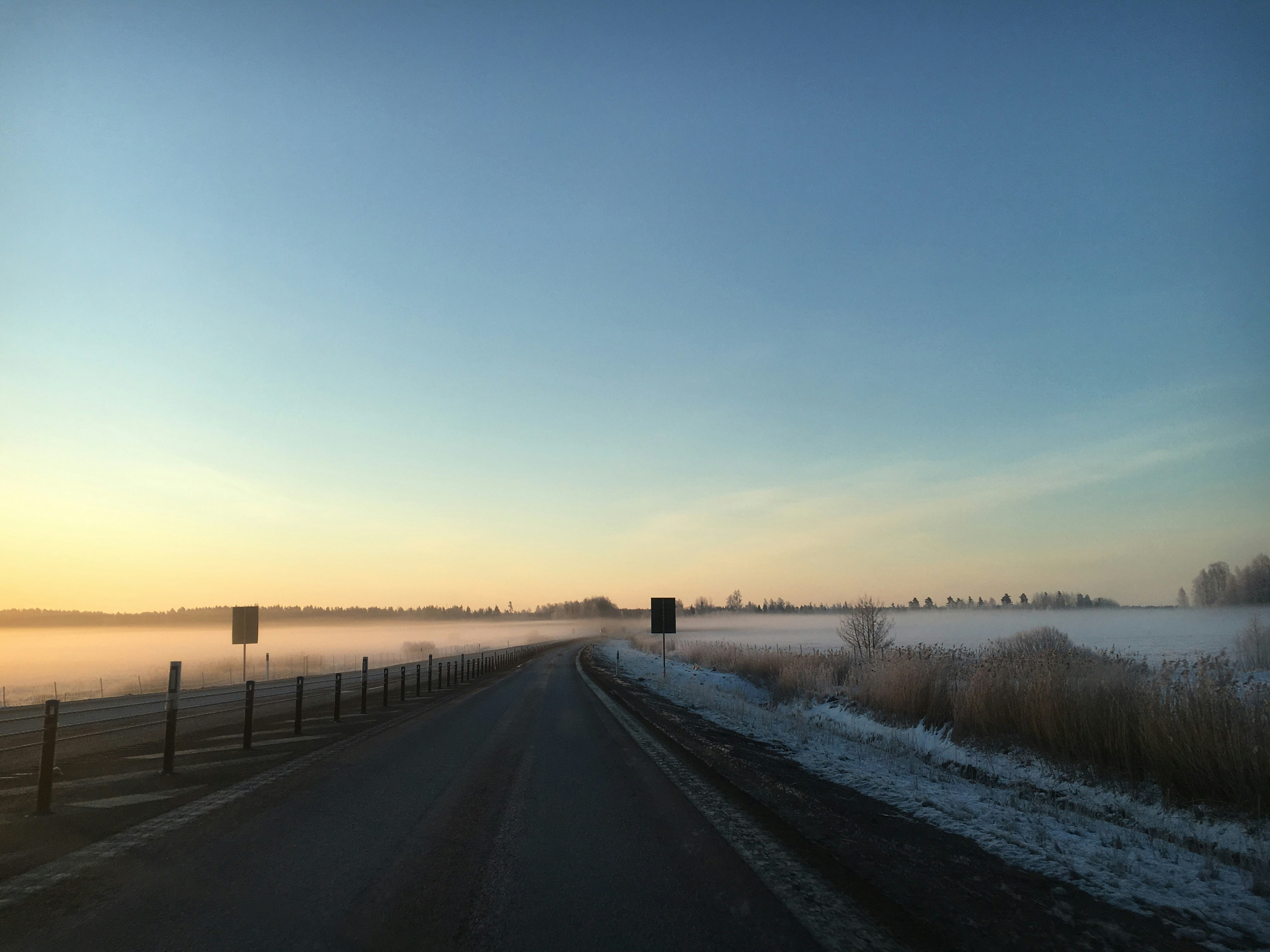 Road stretching into a misty horizon with frosty fields under a clear morning sky.