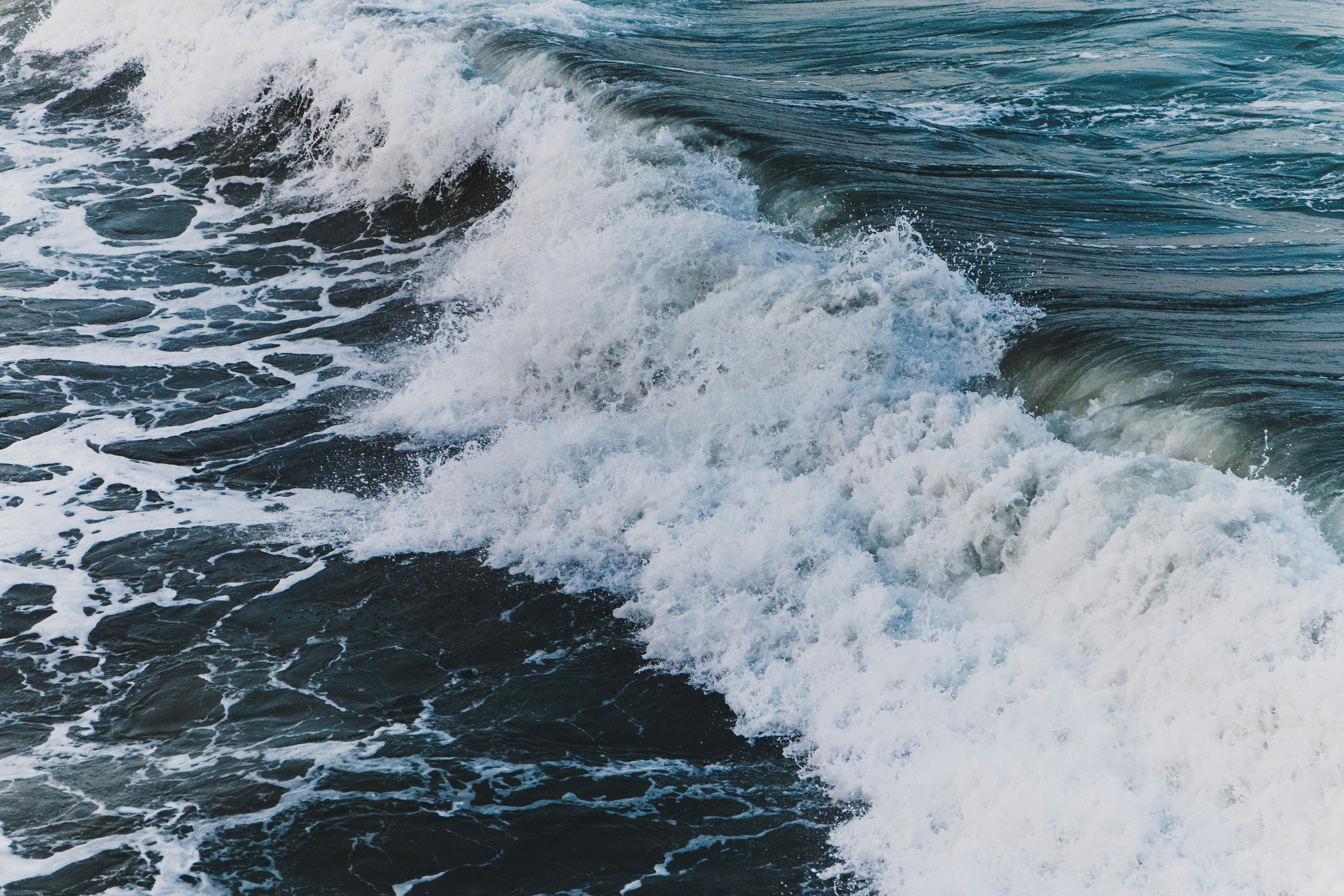 Cascading ocean waves crash with foamy crests along a rugged shoreline.