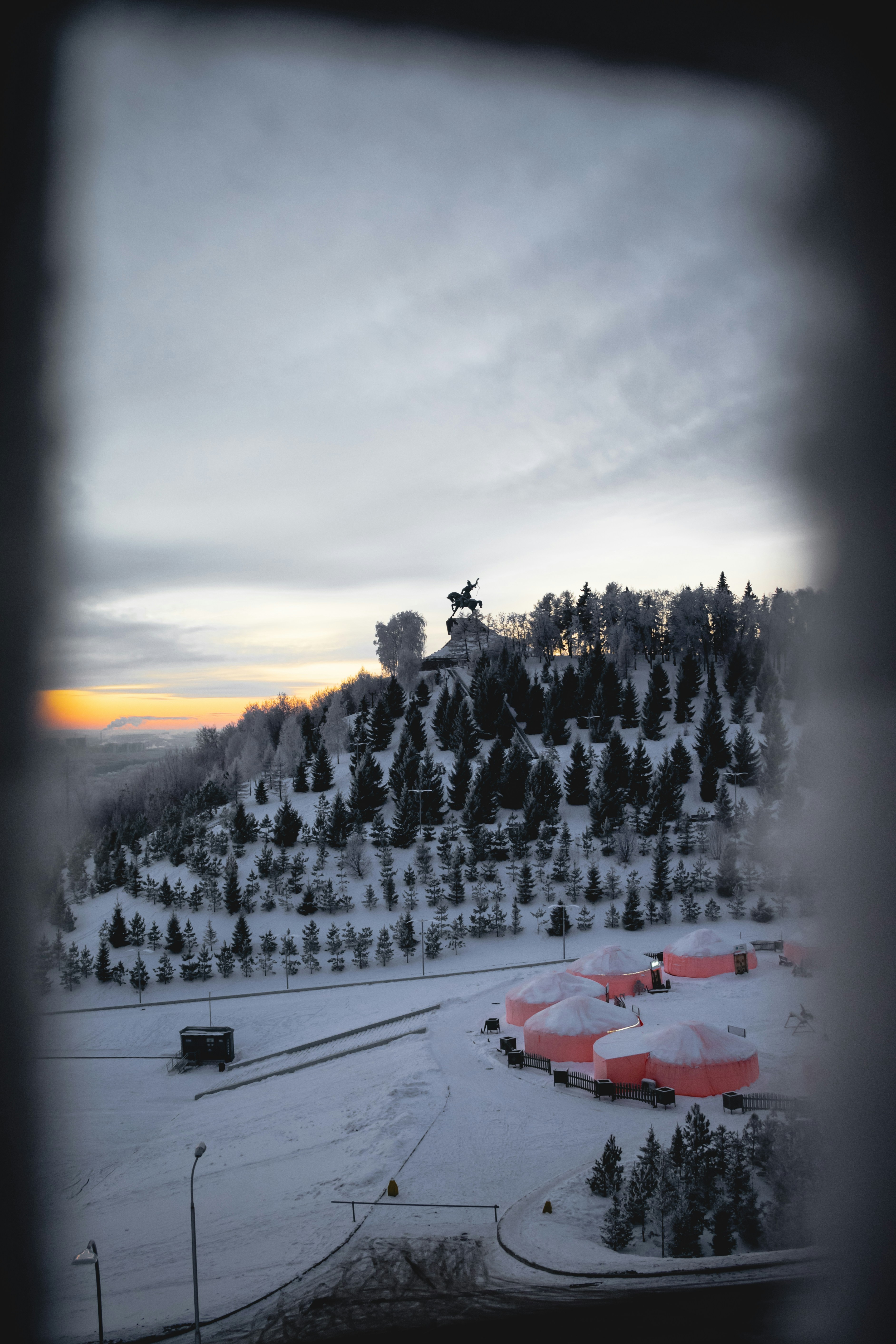 Snow-capped hilltop statue framed by frosted pines at dusk