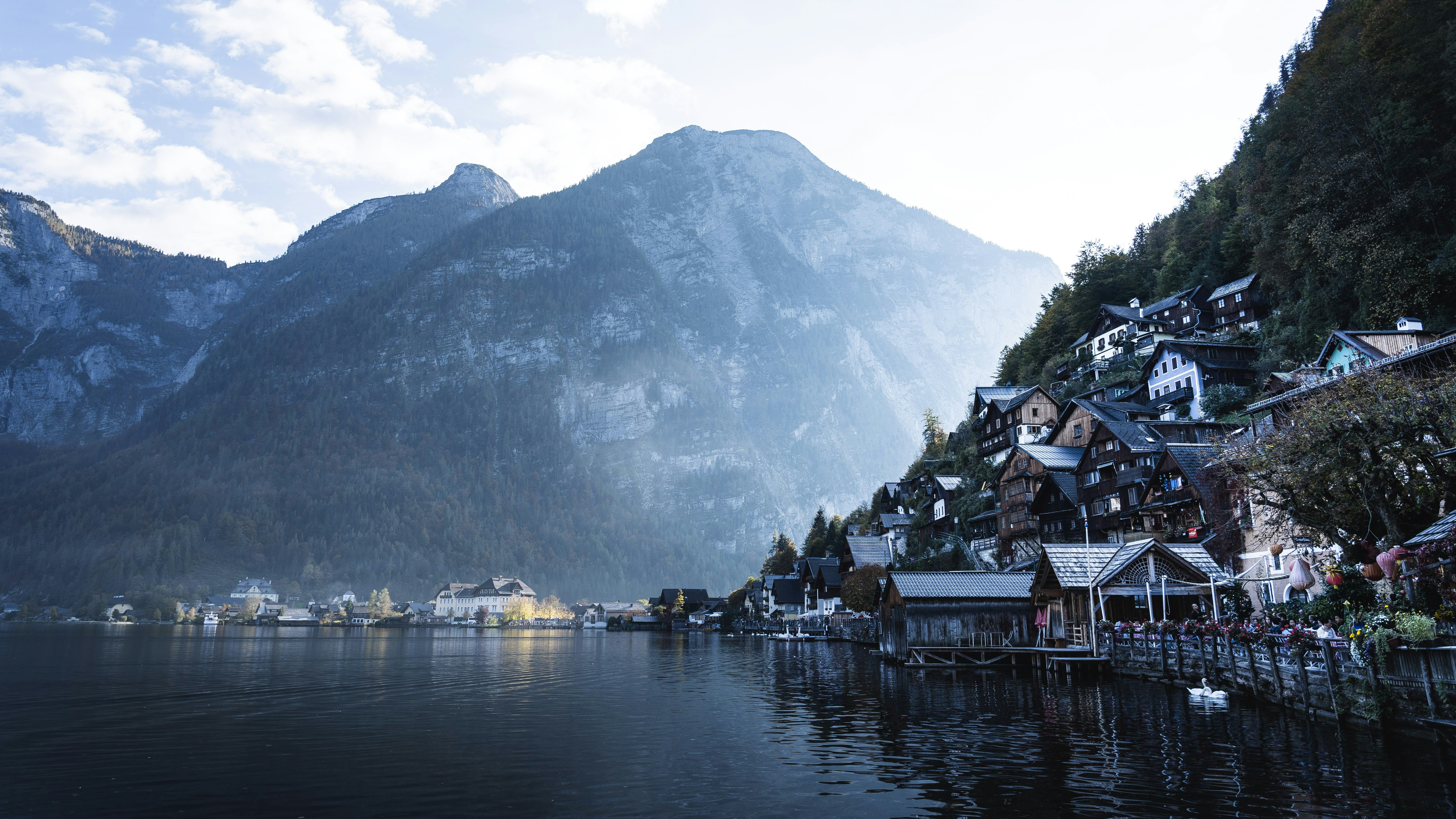 Charming village nestled against a mountain, reflecting on a calm lake under soft morning light.