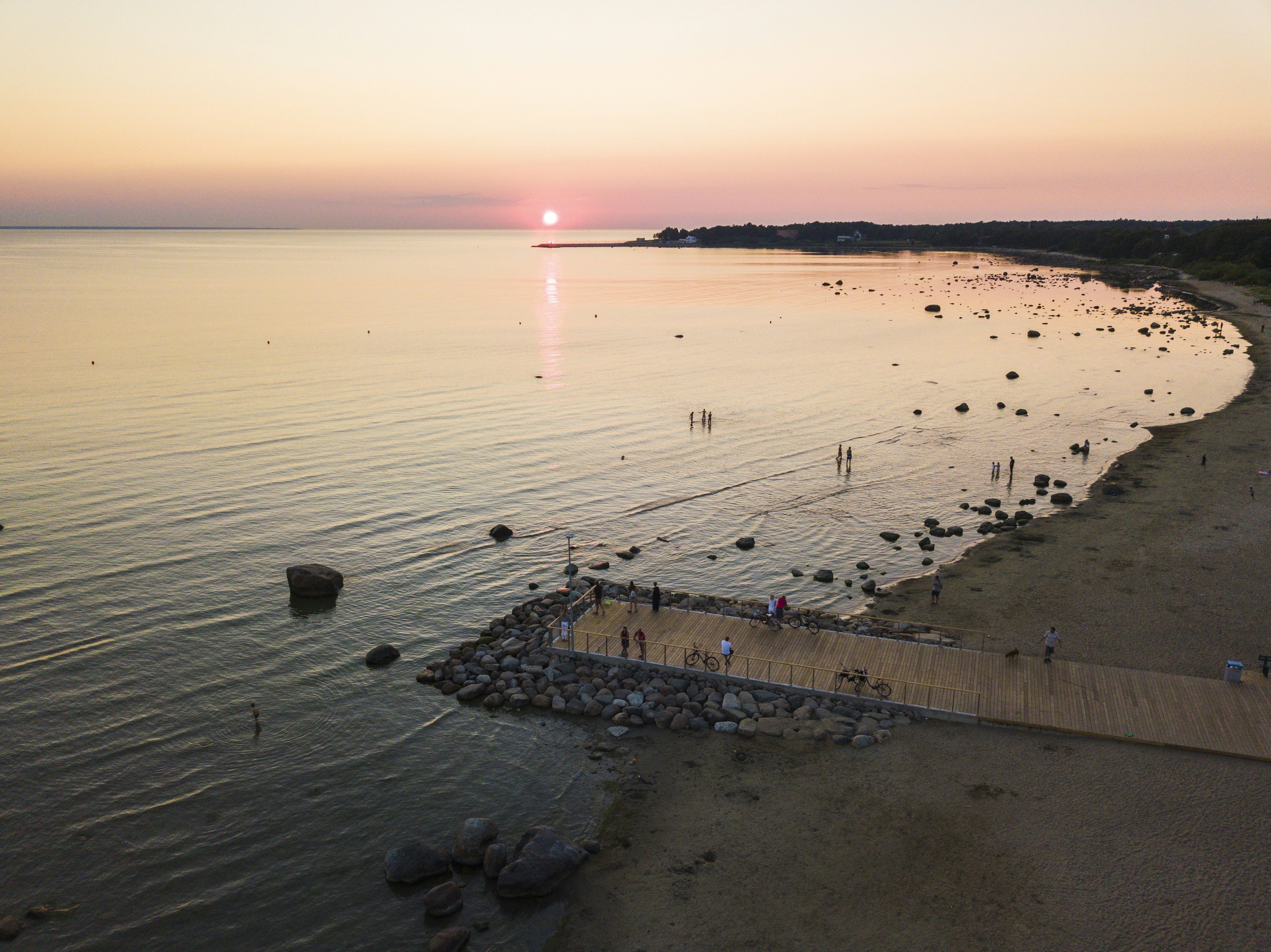 Sunset over a tranquil beach with gentle waves and scattered visitors along the shoreline.