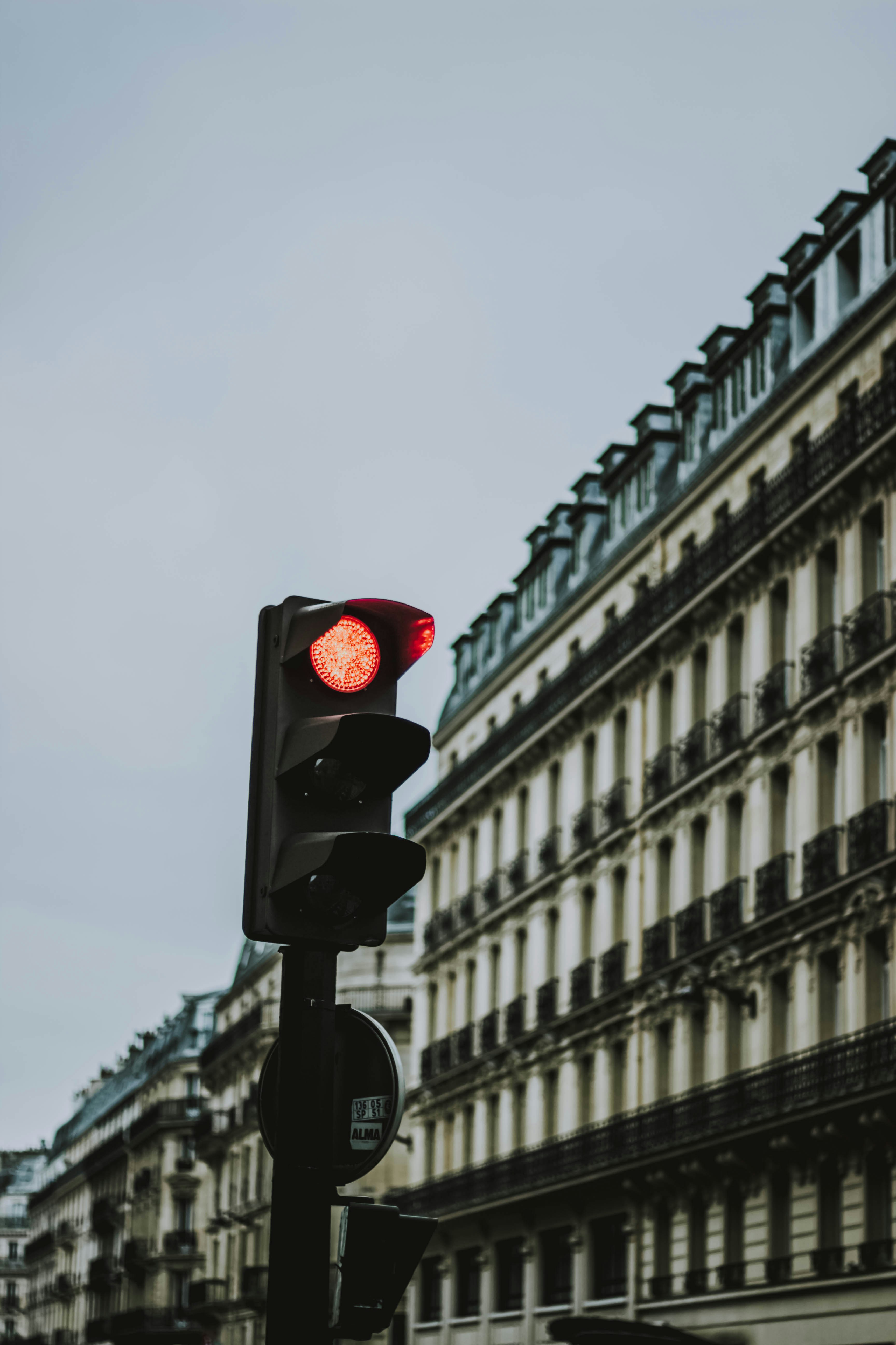 Red traffic light stands against a backdrop of elegant urban architecture, signaling a moment of stillness in the bustling city.