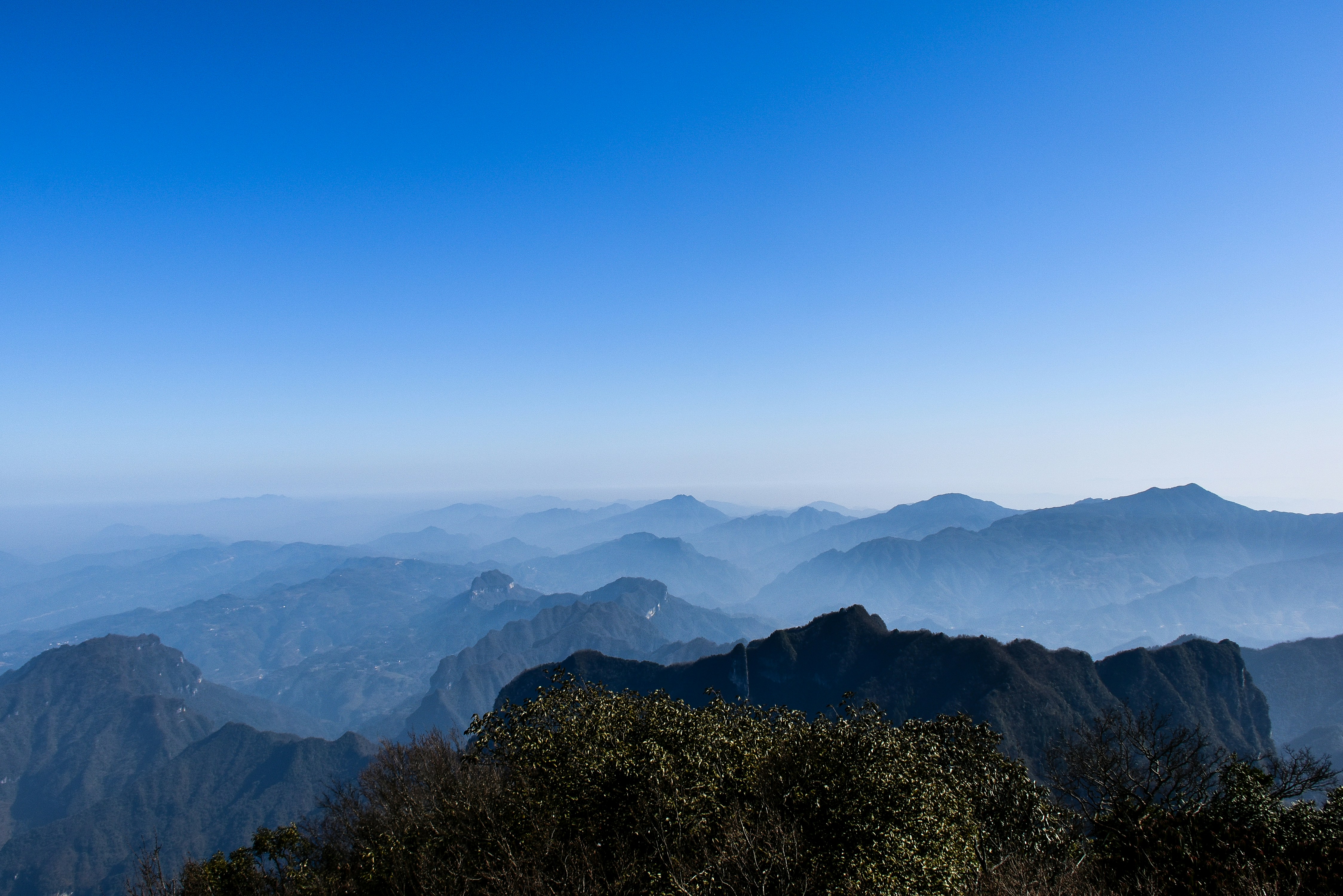 Mountain range with misty layers beneath a clear blue sky.