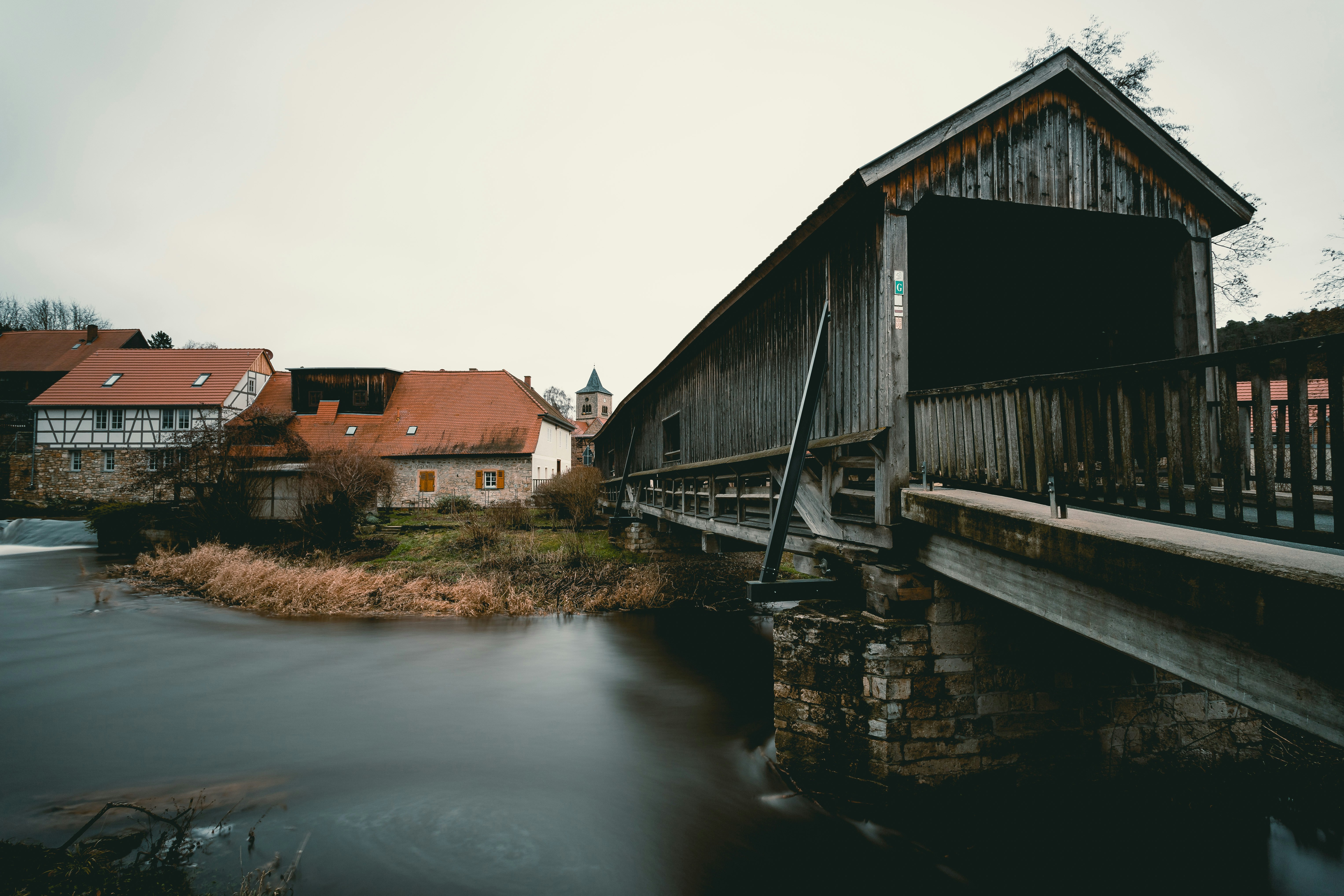 Timber Bridge on the Quiet River: A Village Under Gray Skies