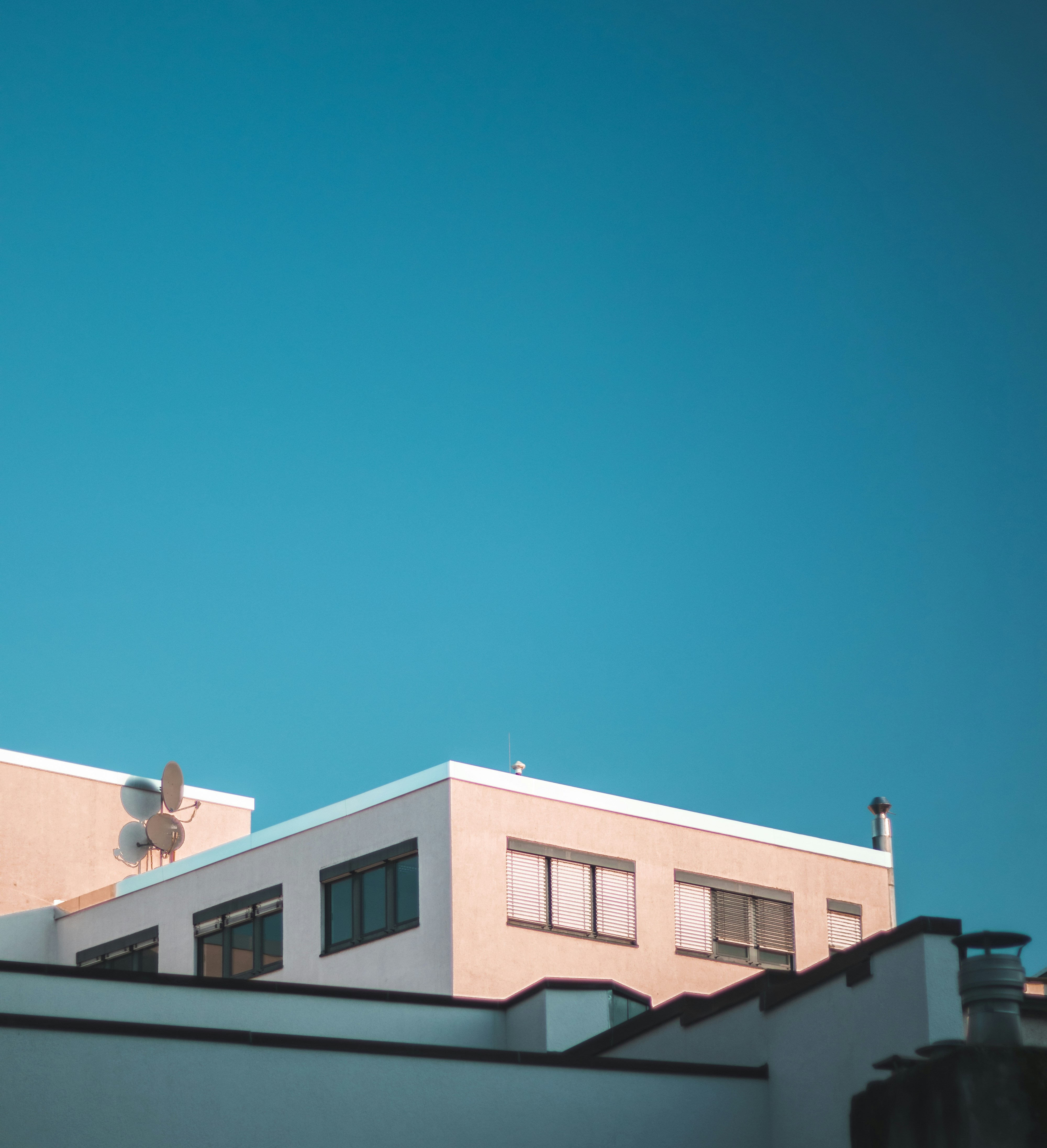 Modern building rooftops with satellite dishes under a vivid blue sky.