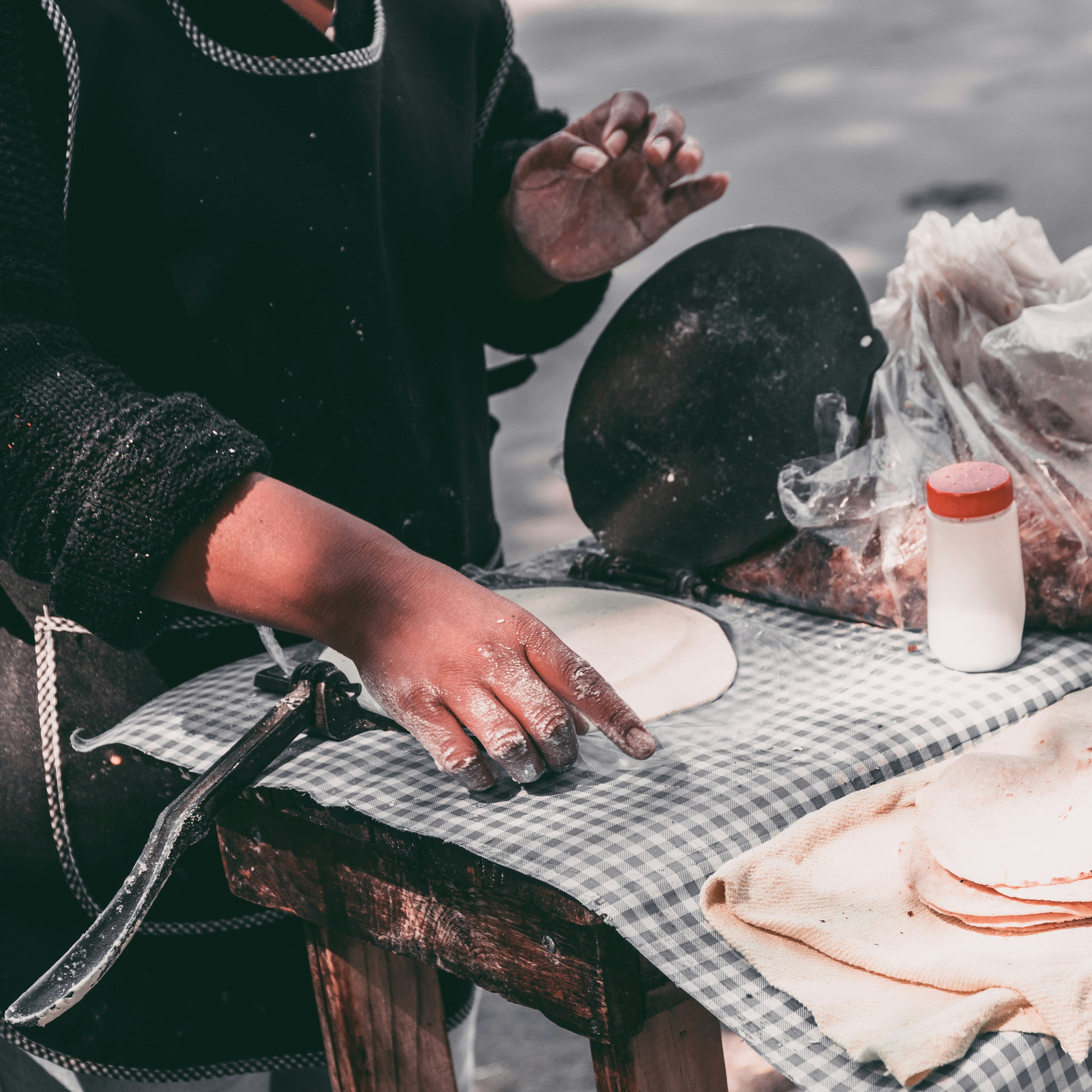 A hands-on moment in food preparation, showcasing a person skillfully shaping dough on a checkered cloth-covered table, surrounded by ingredients and utensils.