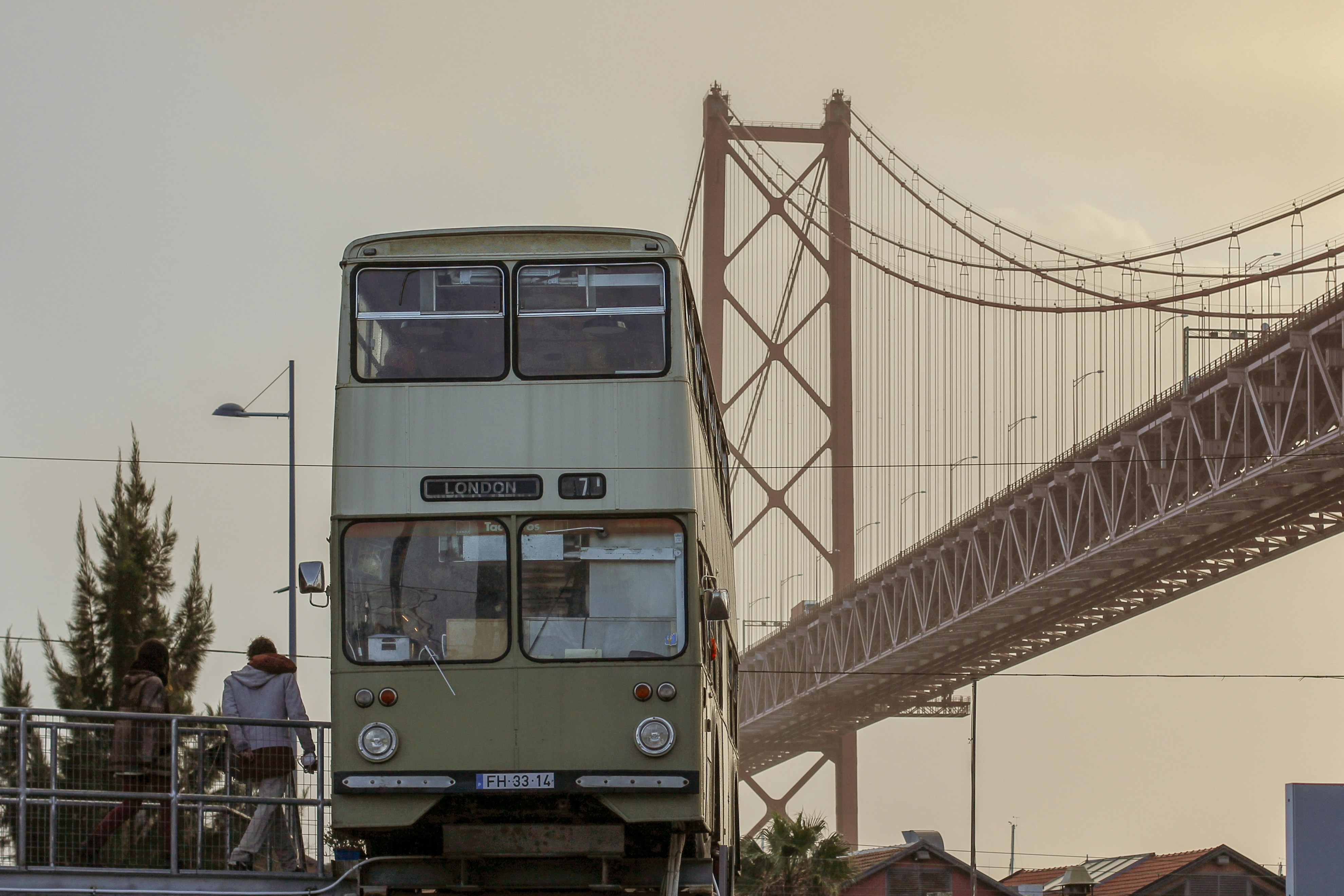 Green double-decker tram under a steel arch at dusk