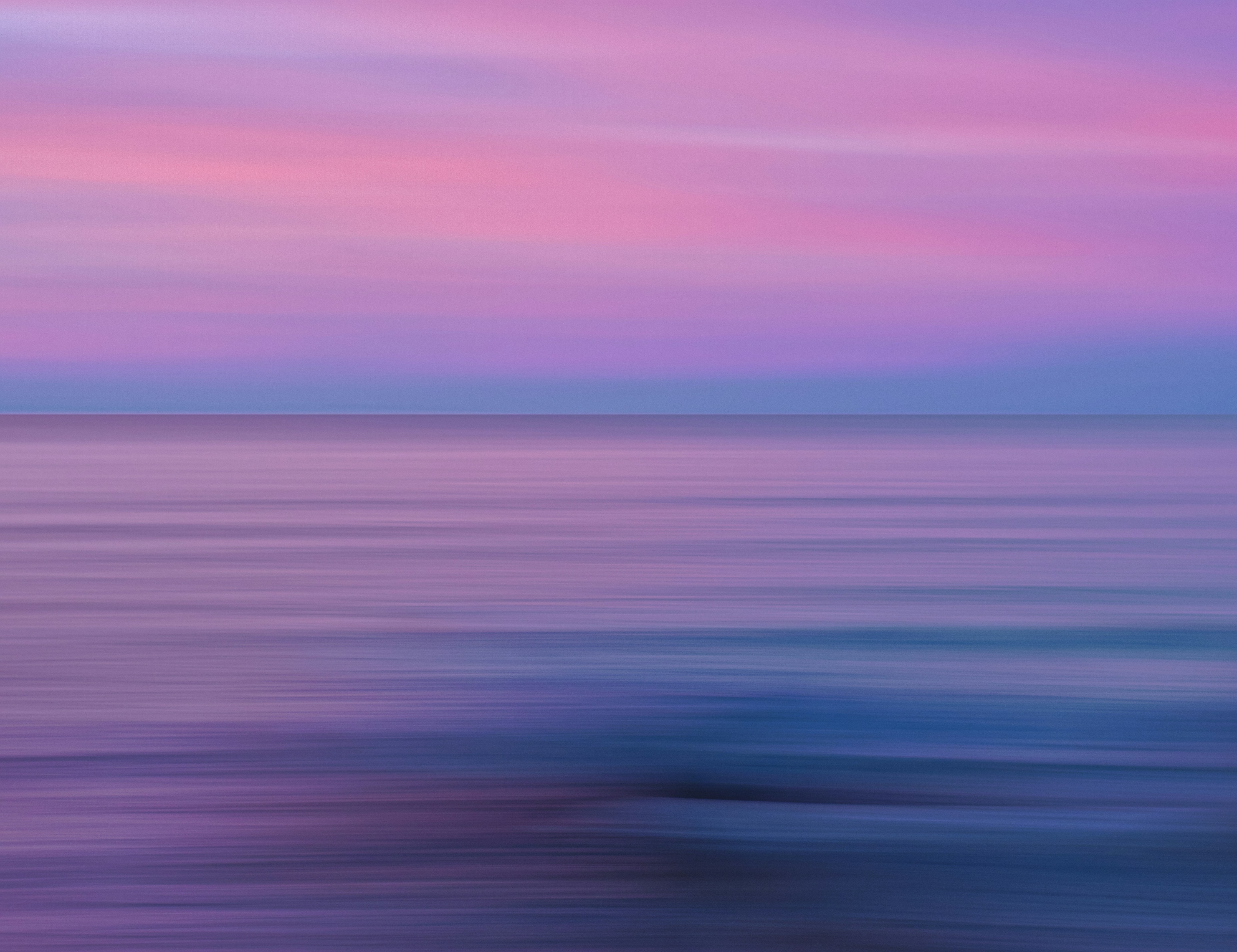 Soft hues of pink and purple blend over a tranquil ocean at dusk, creating a serene abstract landscape.