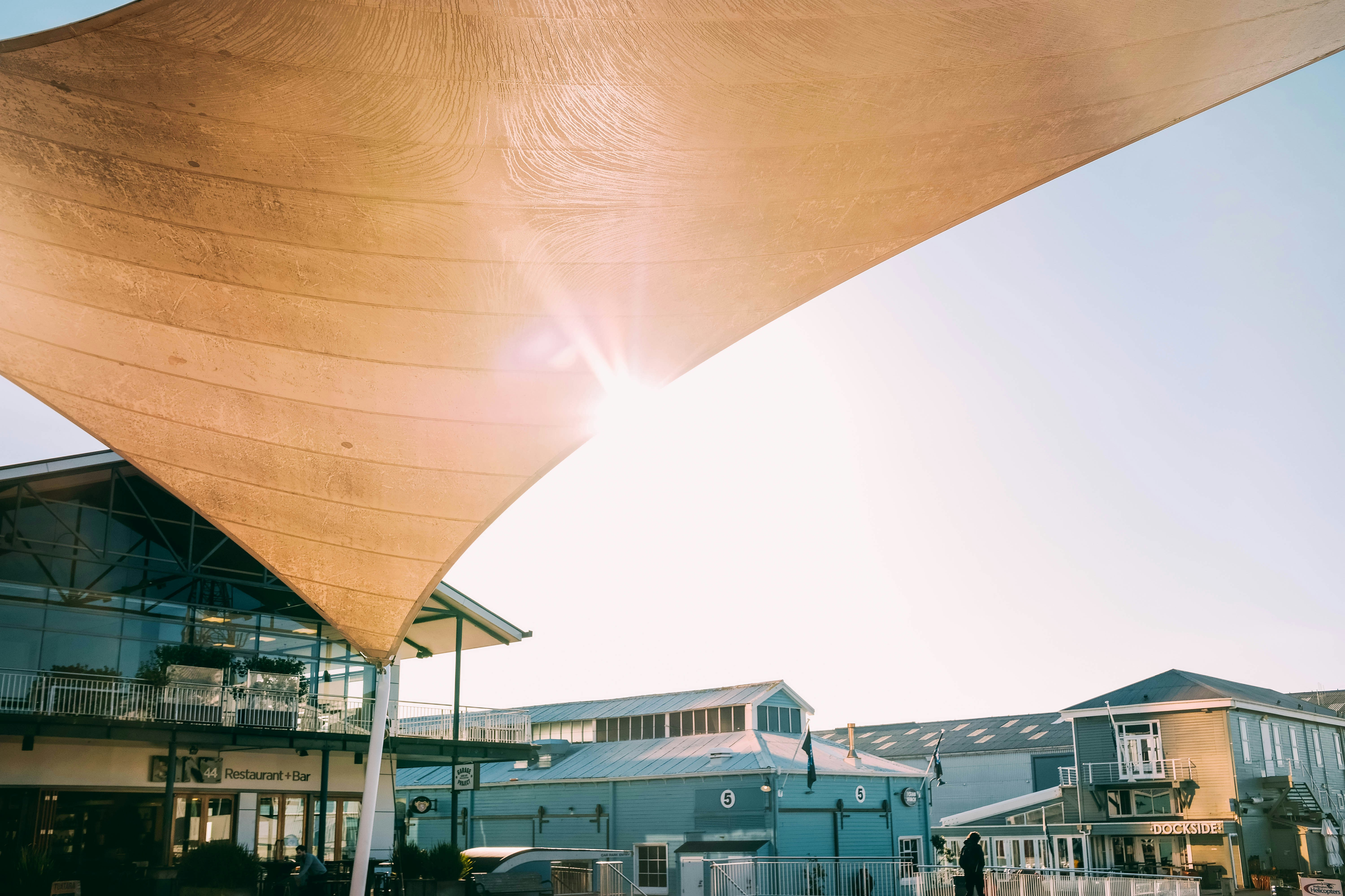 Under the Sail: Sunlit Canopy Over a Busy Waterfront