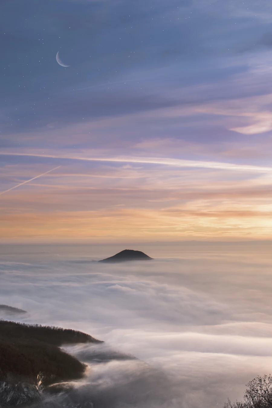 Pastel dawn hues blanket the sky as a lone island rises through a sea of clouds. A crescent moon and scattered stars punctuate the tranquil expanse.
