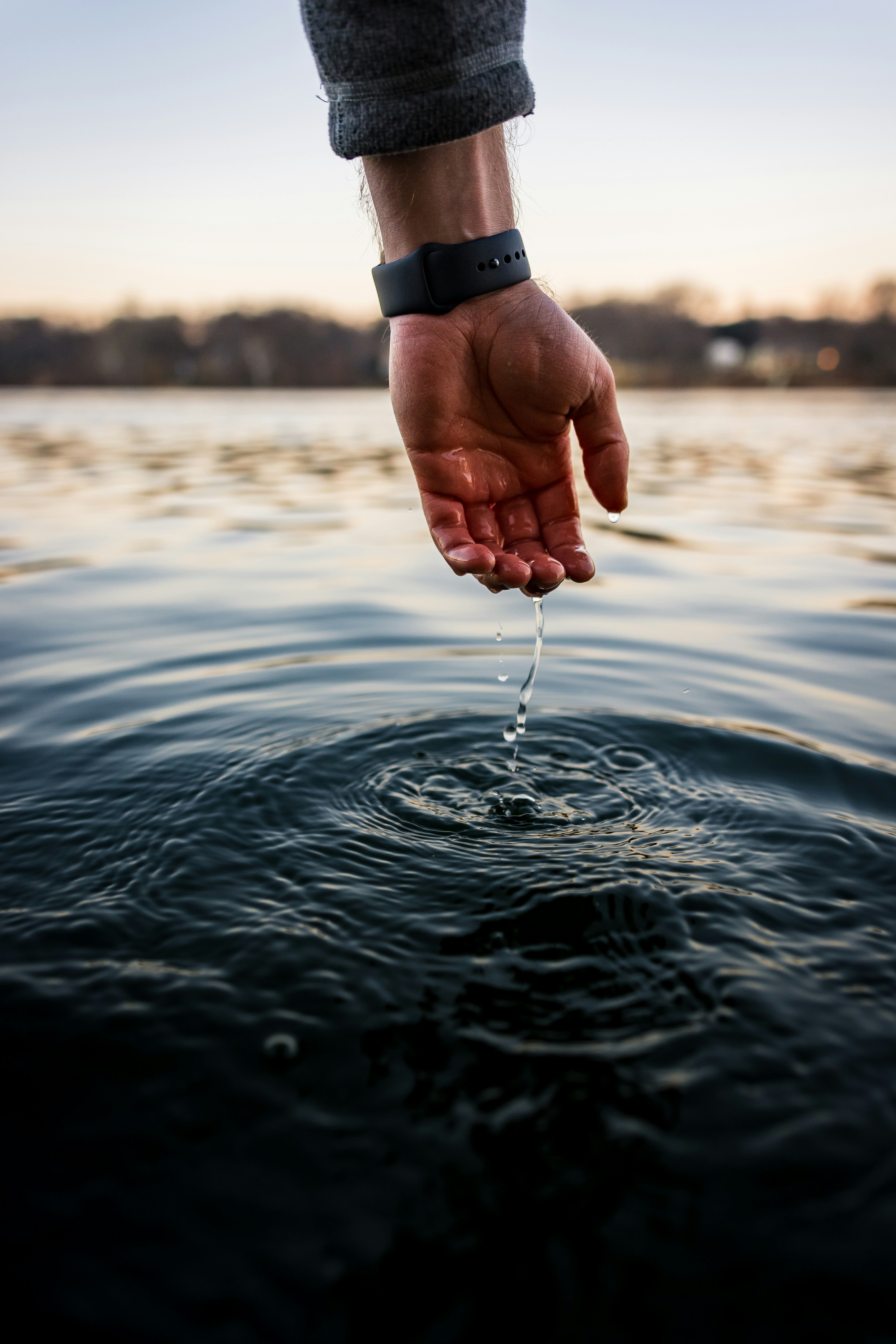 A hand gently releases water droplets into a serene lake, creating ripples on the surface. The tranquil setting captures a fleeting moment of interaction with nature.
