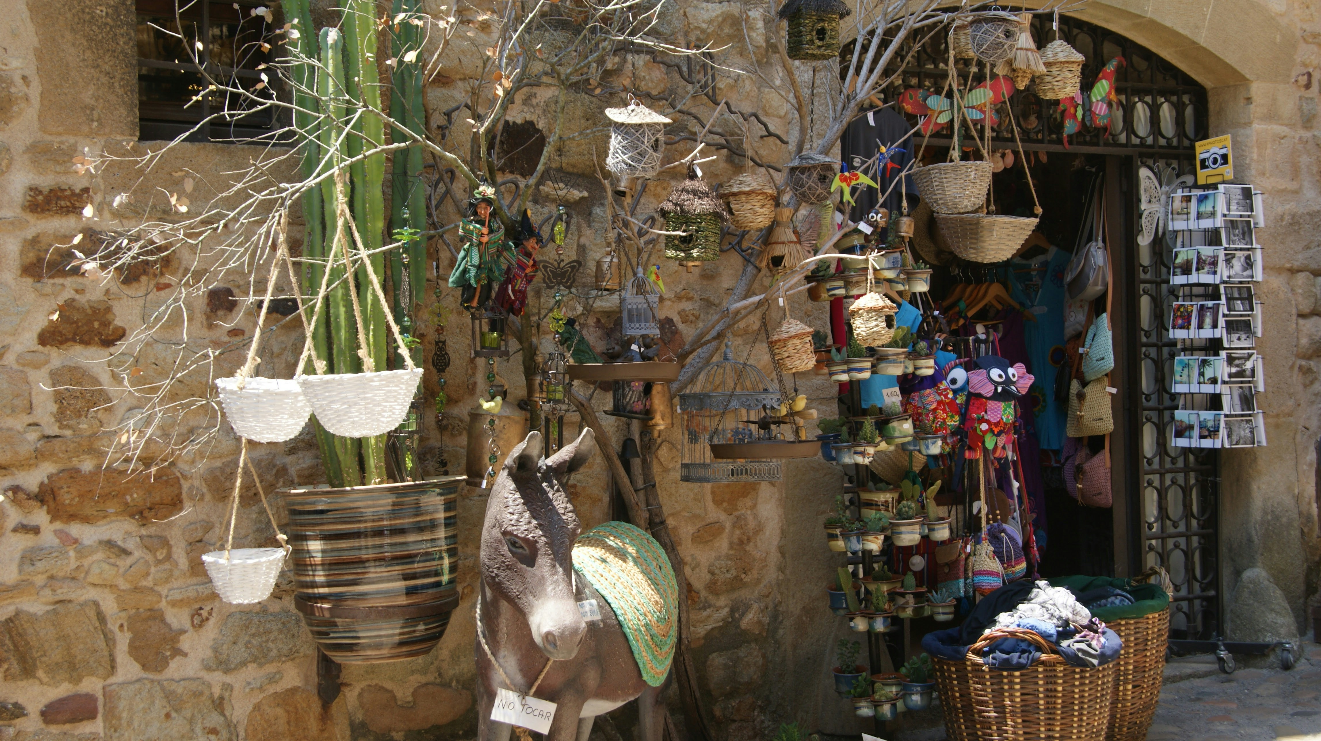 Colorful display of handmade crafts and decorations outside a quaint shop, featuring hanging planters and a decorative horse statue.