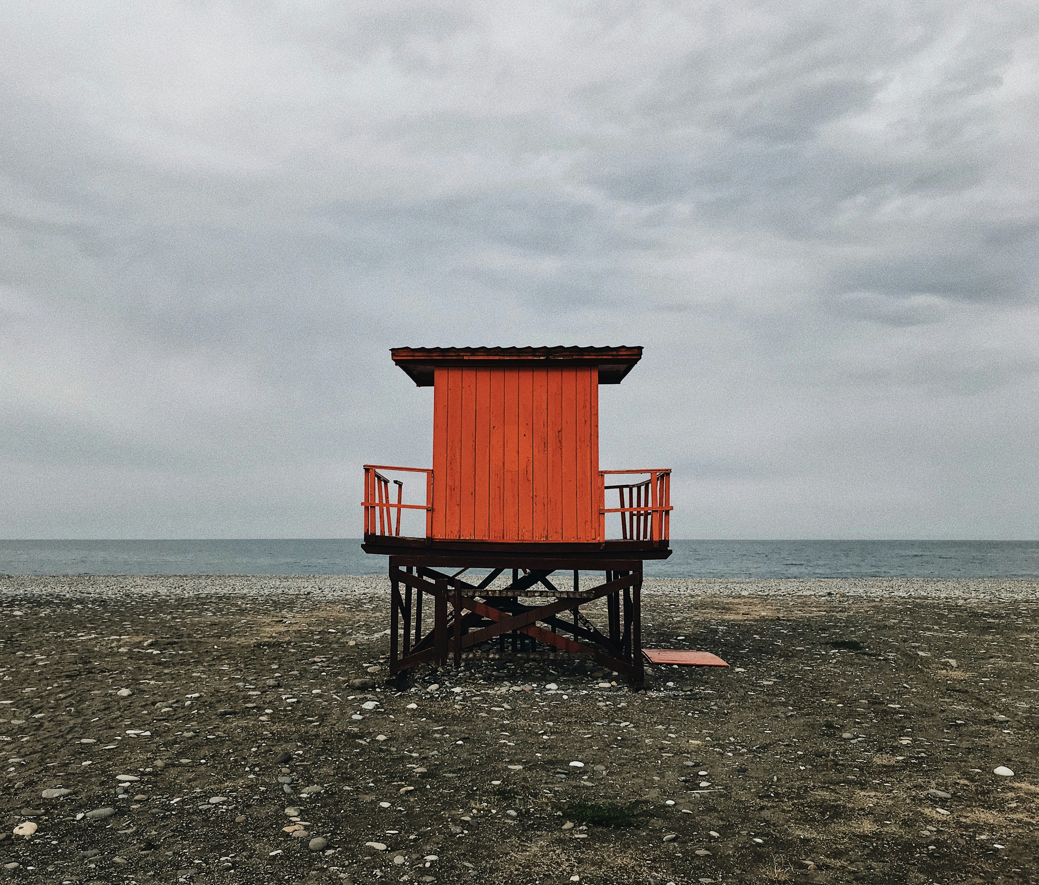 Crimson Lifeguard Hut Anchored on a Pebble Beach