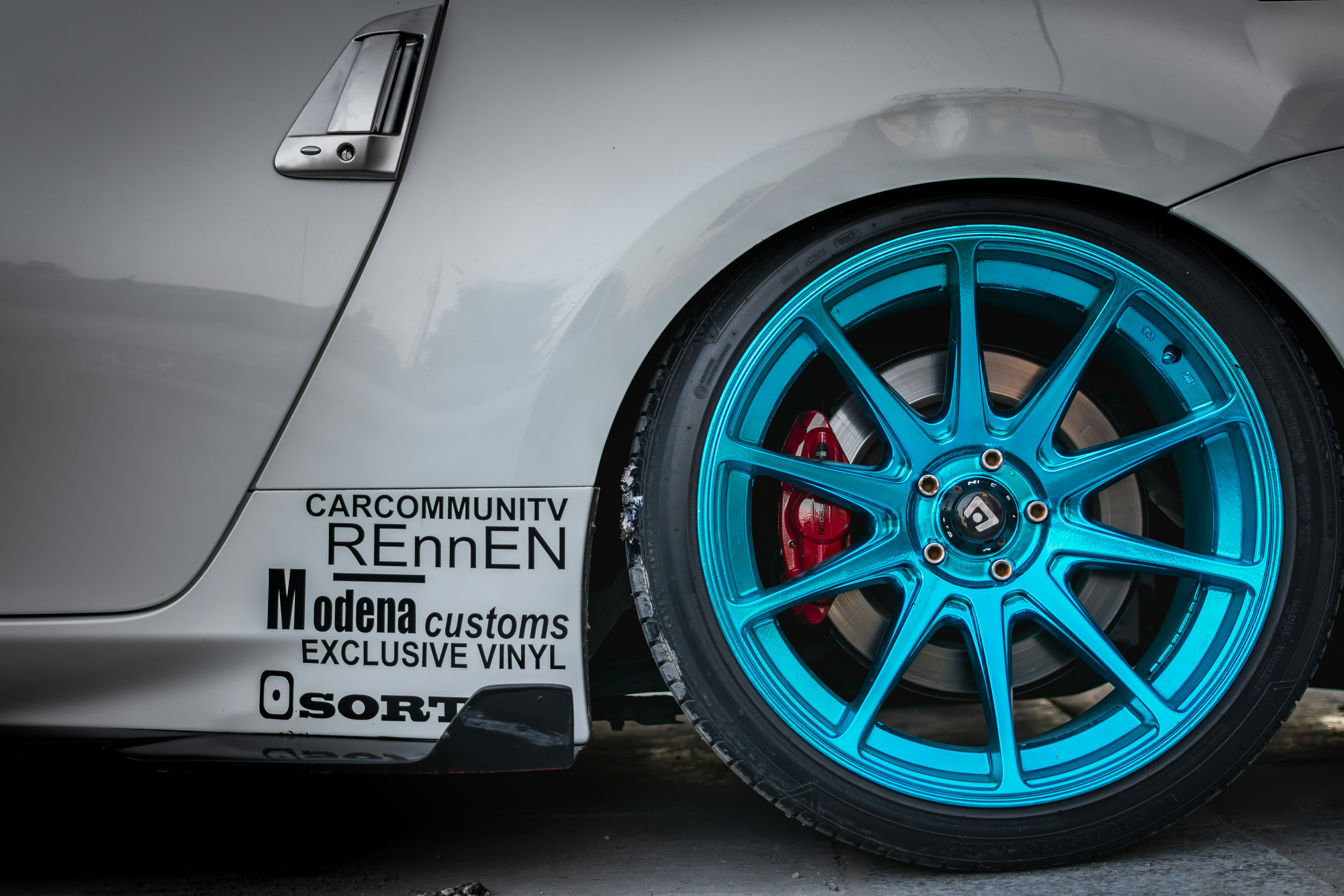 Close-up of a customized car wheel featuring vibrant turquoise spokes and detailed brake calipers, showcasing automotive artistry.