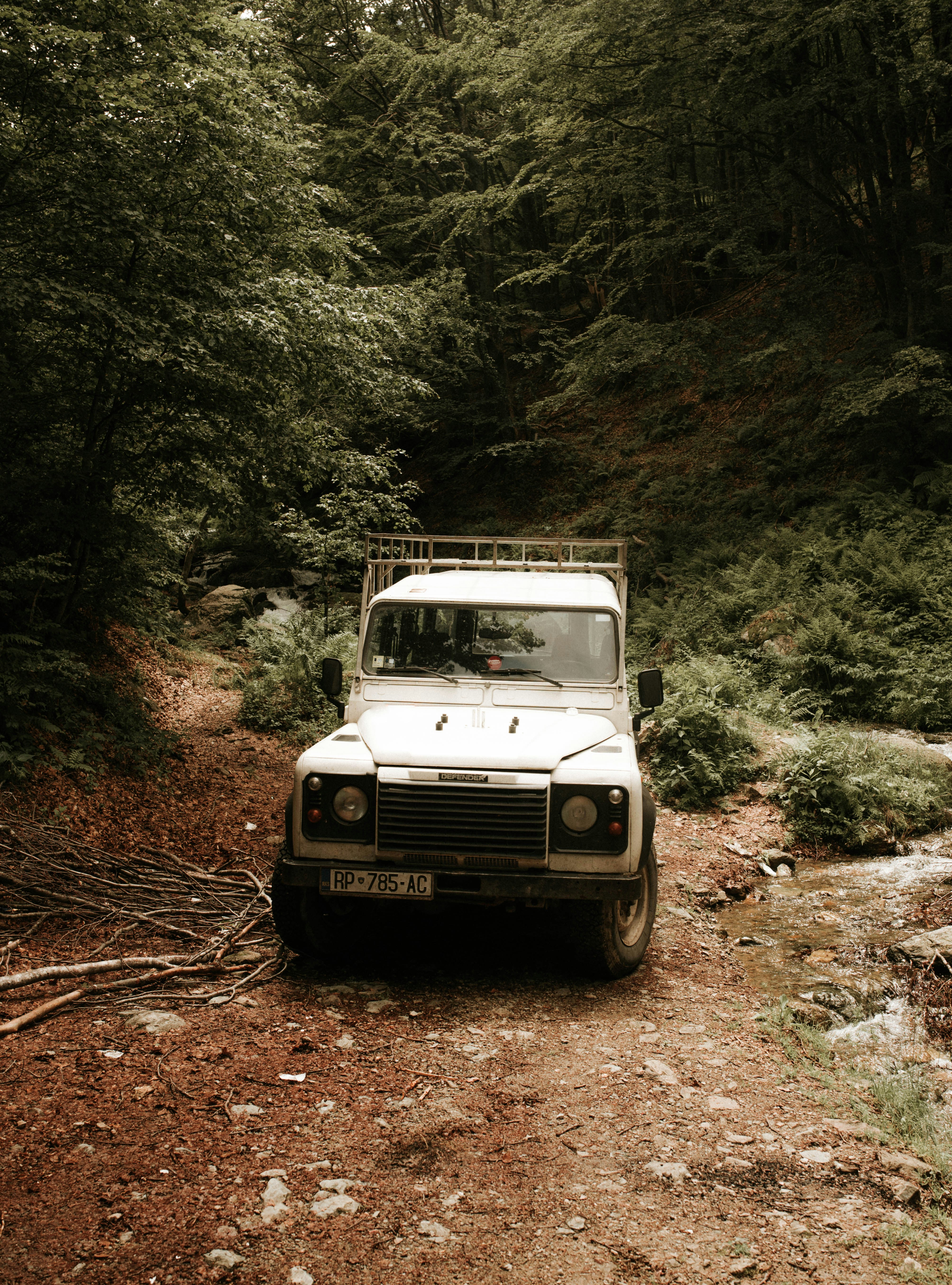 A vintage off-road vehicle parked on a forest path, surrounded by lush greenery and a gentle stream nearby.