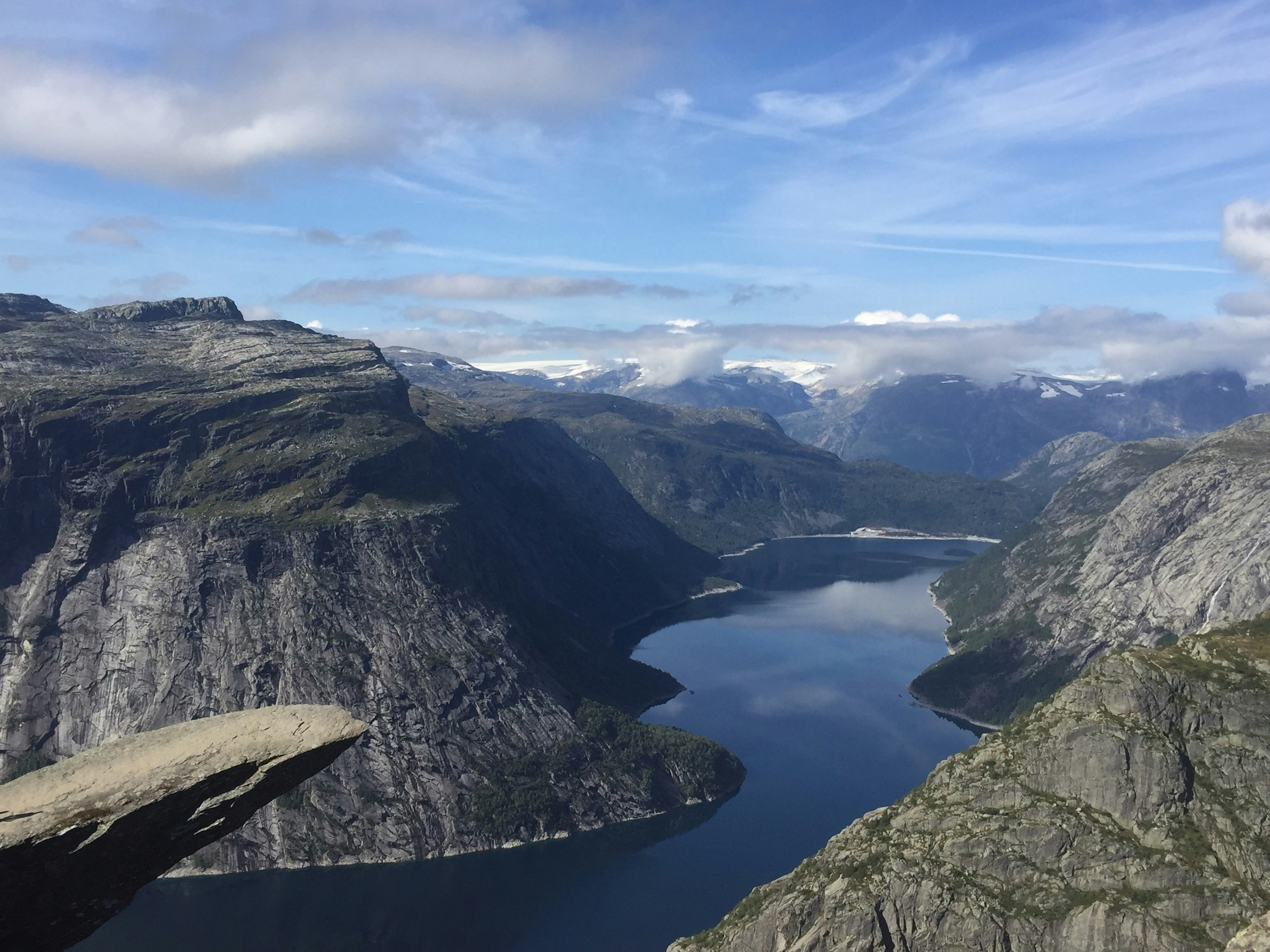 Steep cliffs frame a serene fjord under a bright blue sky with scattered clouds.