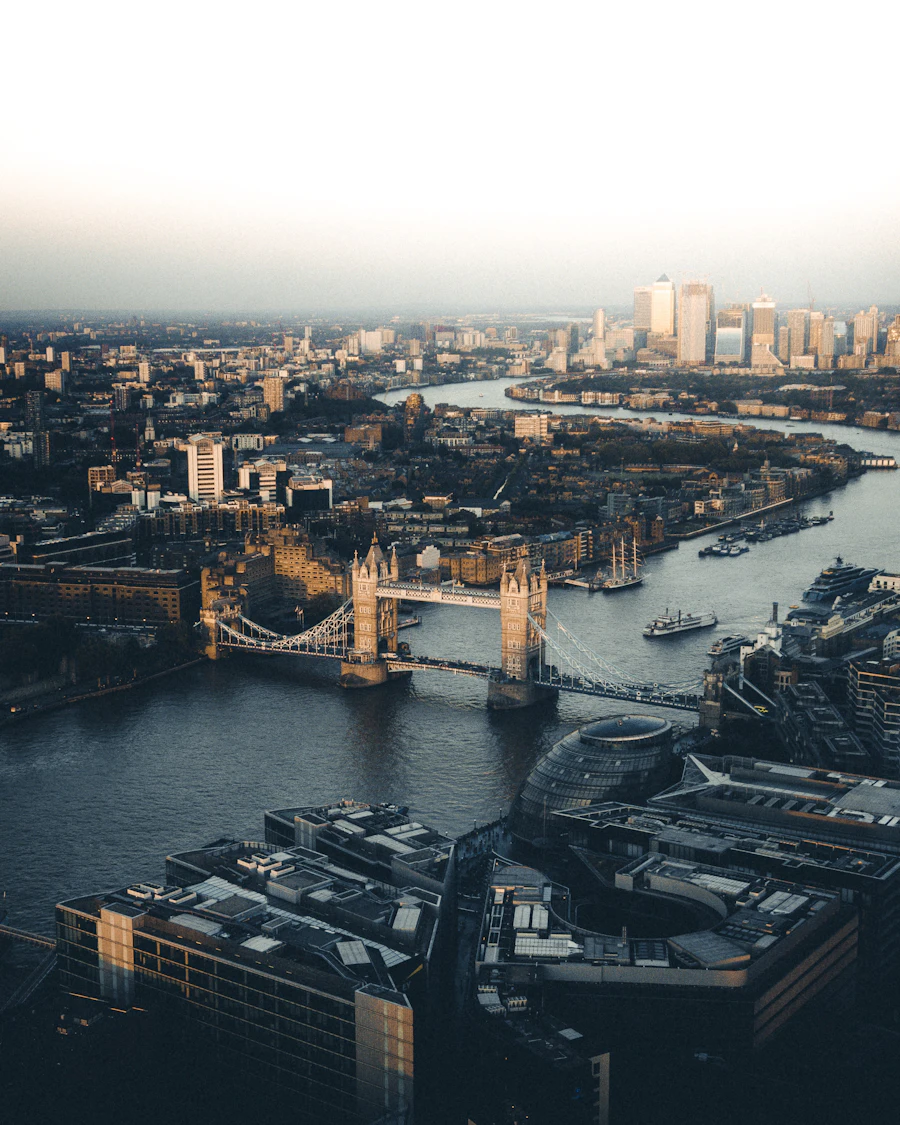 Aerial cityscape of London highlighting Tower Bridge spanning the Thames at dusk, with surrounding buildings and boats along the river.