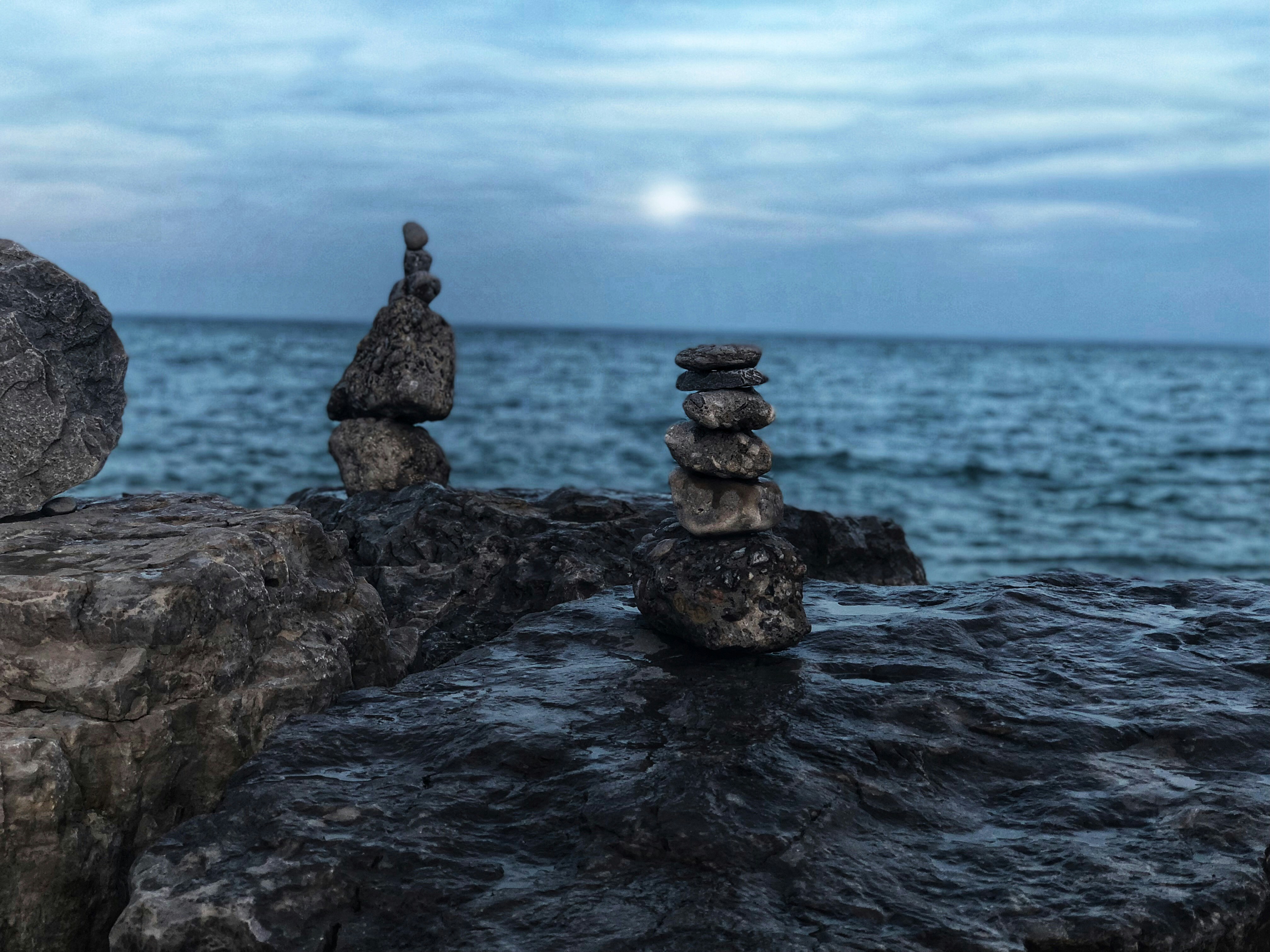 Balanced Cairns on a Rugged Shore Under a Quiet Blue Horizon