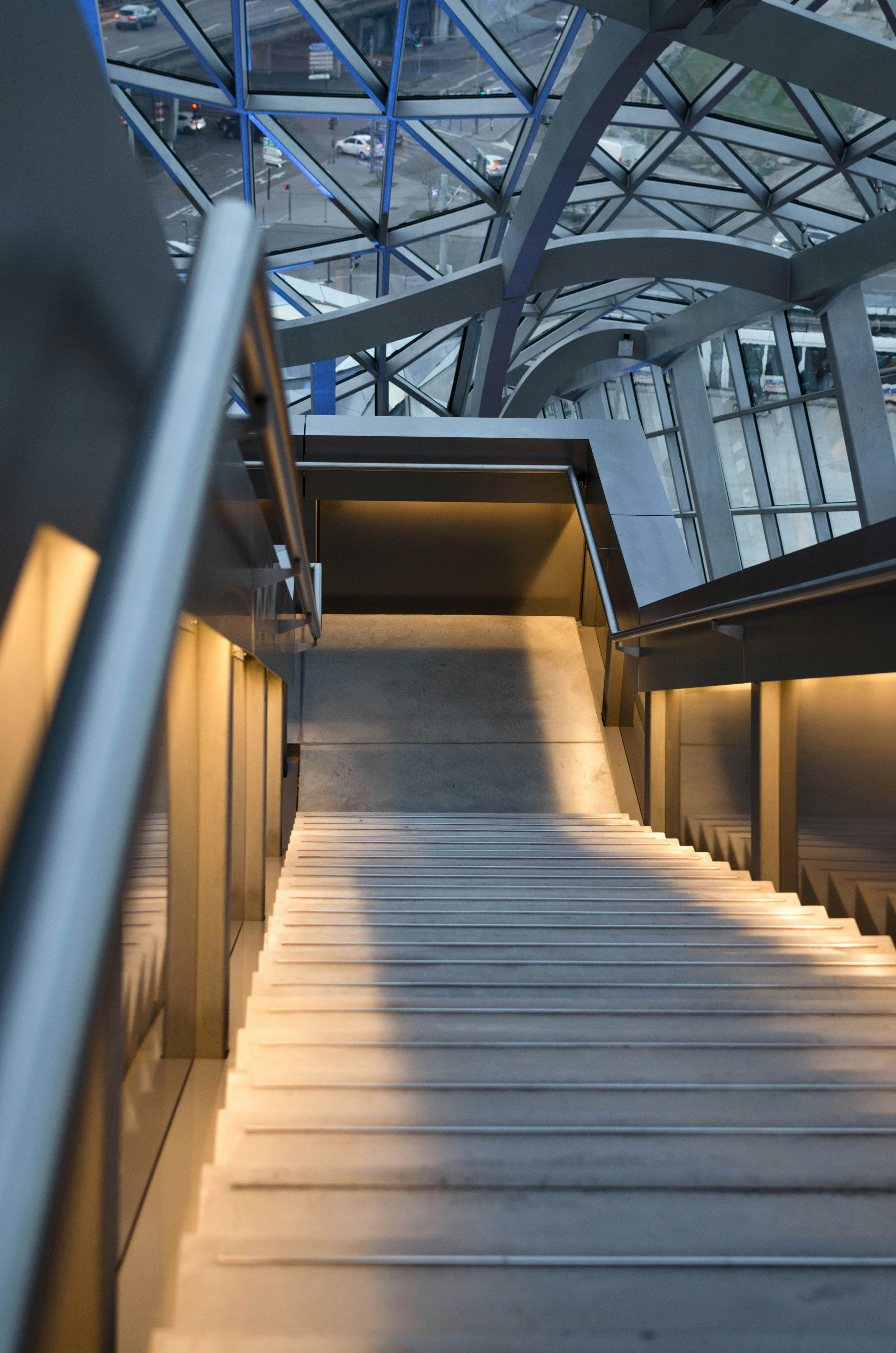 Modern staircase illuminated by warm lighting, leading downwards within a contemporary building. The geometric patterns of the structure create a striking visual narrative.